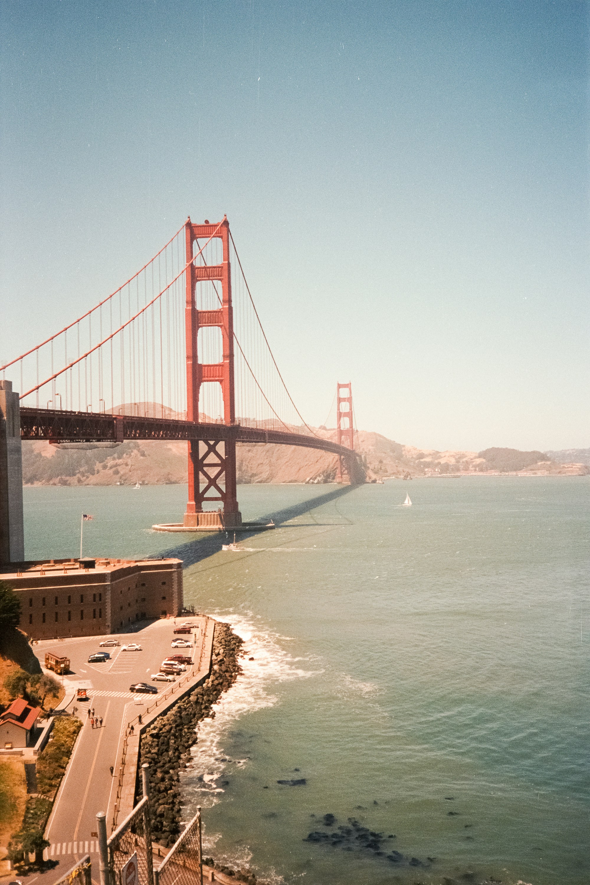 Golden Gate Bridge spanning across the bay with a sailboat gliding beneath, framed by scenic coastal landscape.