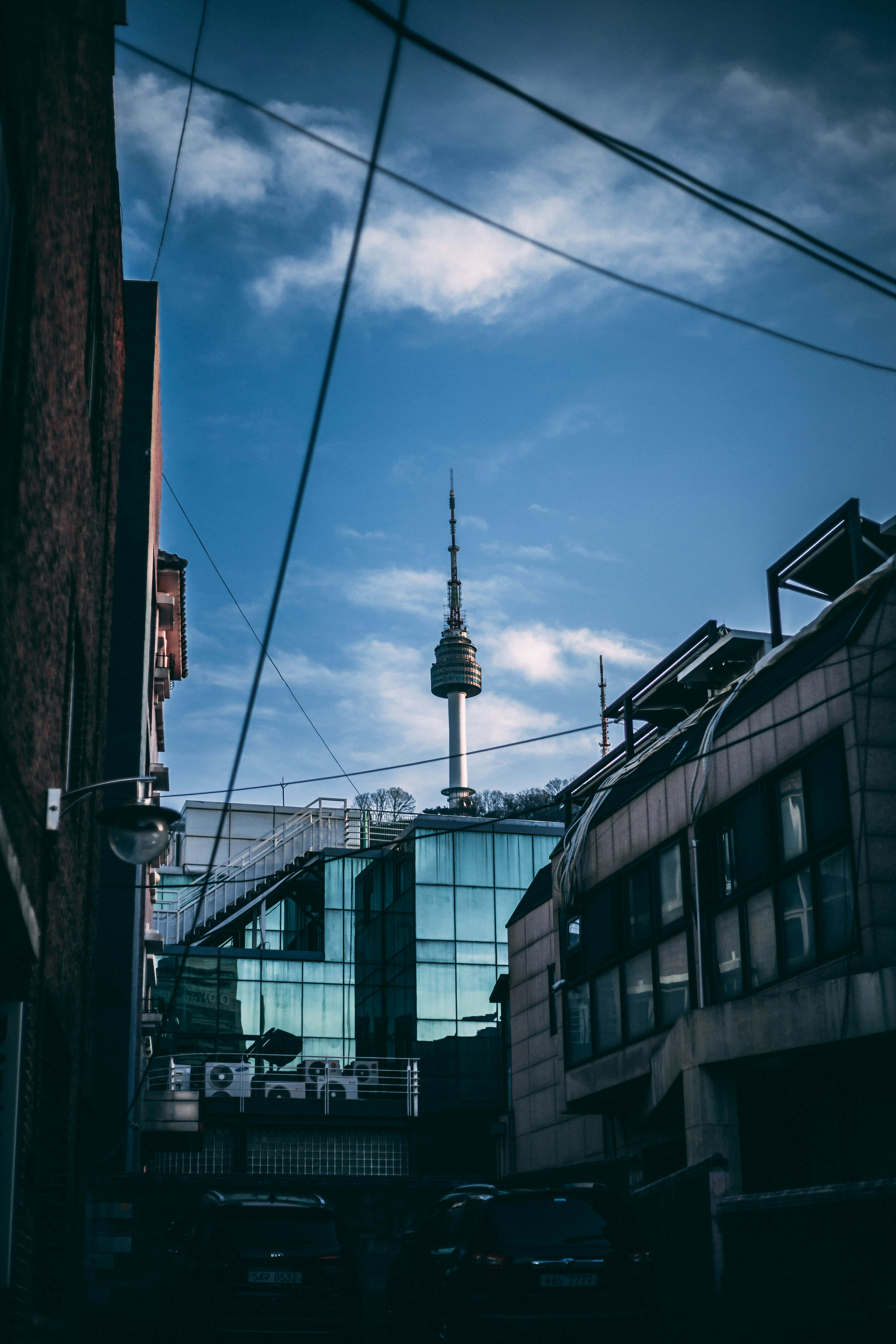 Namsan Tower rises above the urban landscape, framed by modern architecture and power lines, showcasing a blend of nature and city life.