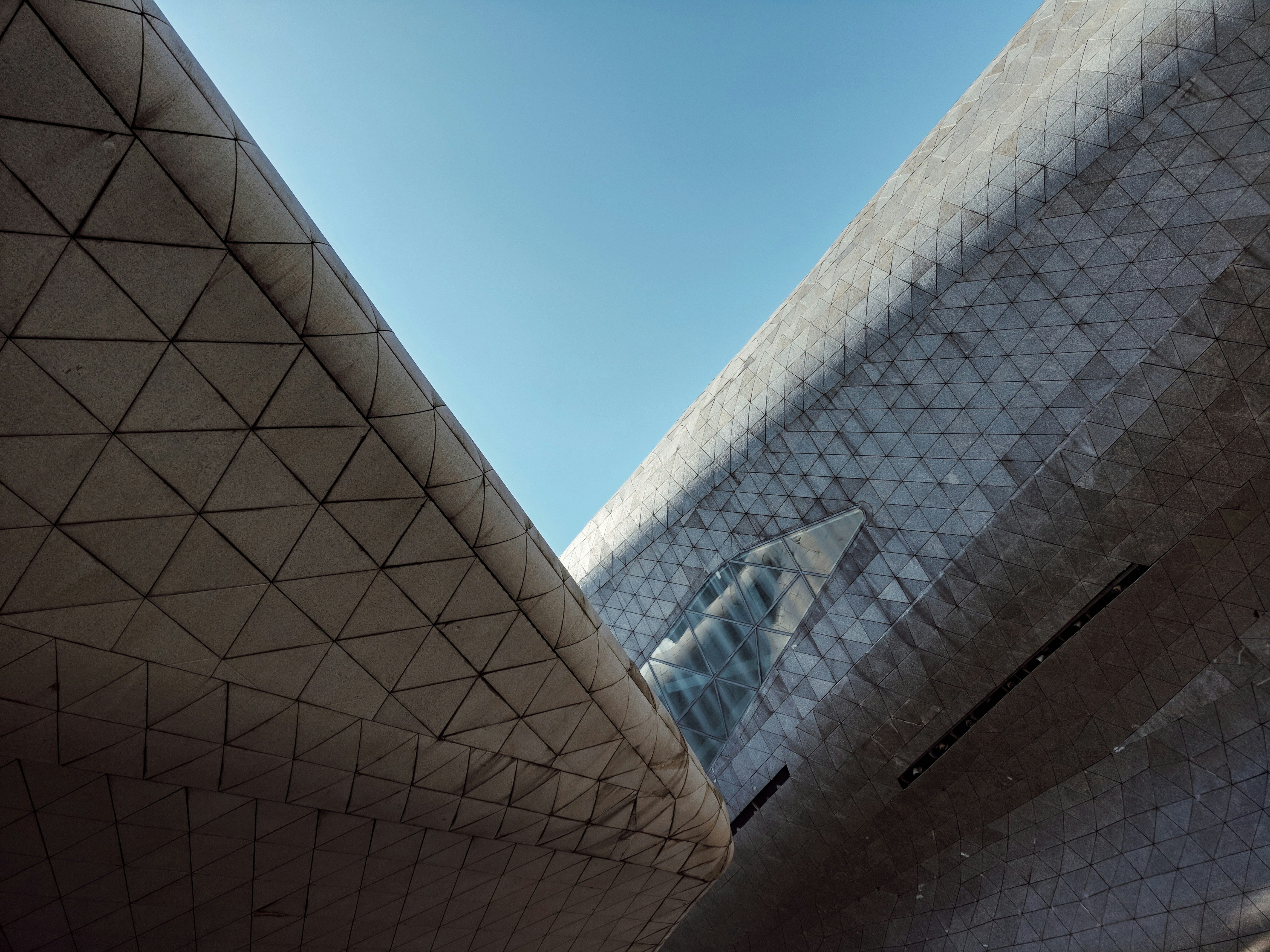 Abstract architectural composition featuring angular forms and textured surfaces against a clear blue sky.