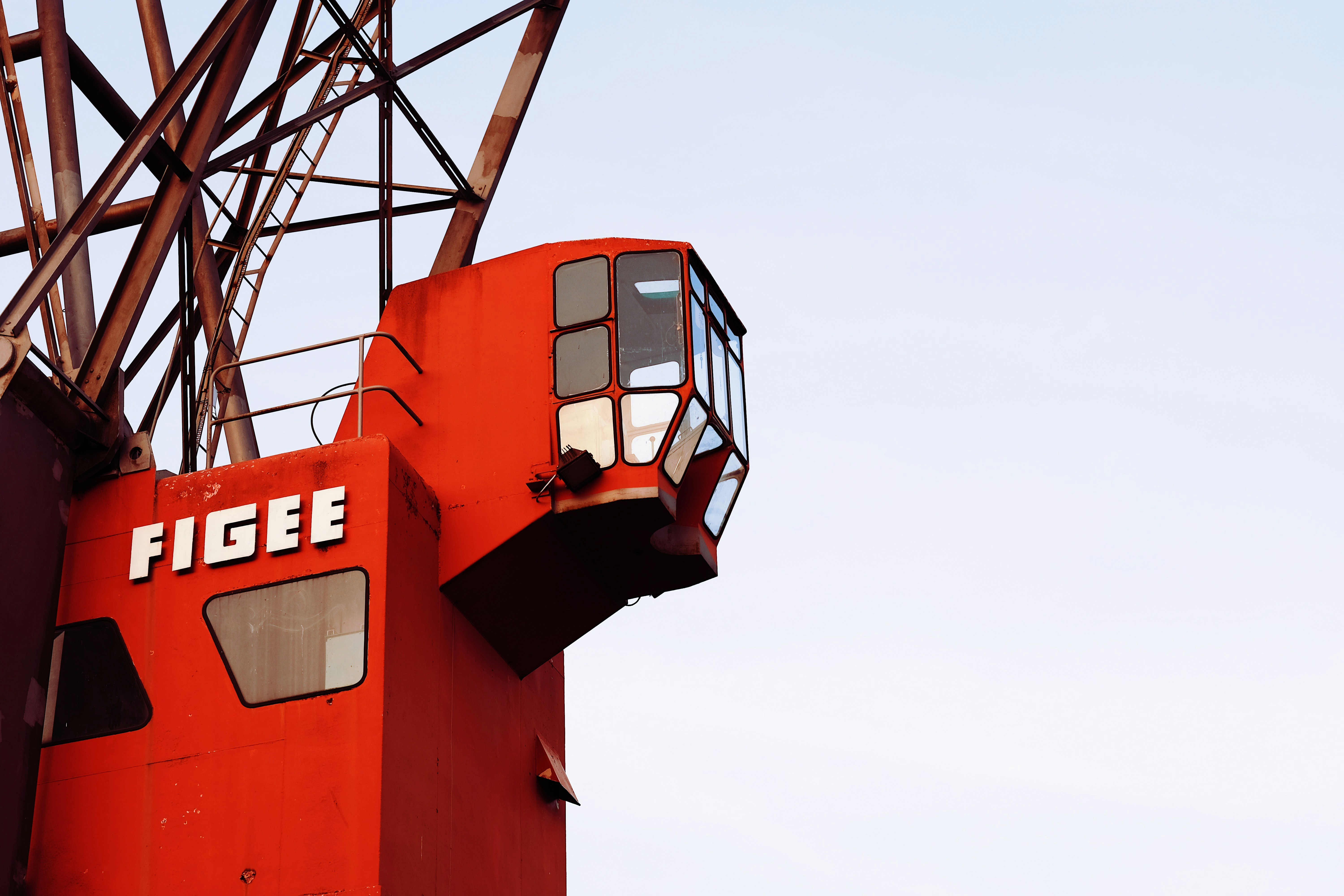 Red crane cab with the word 'FIGEE' prominently displayed, showcasing industrial architecture against a clear sky.