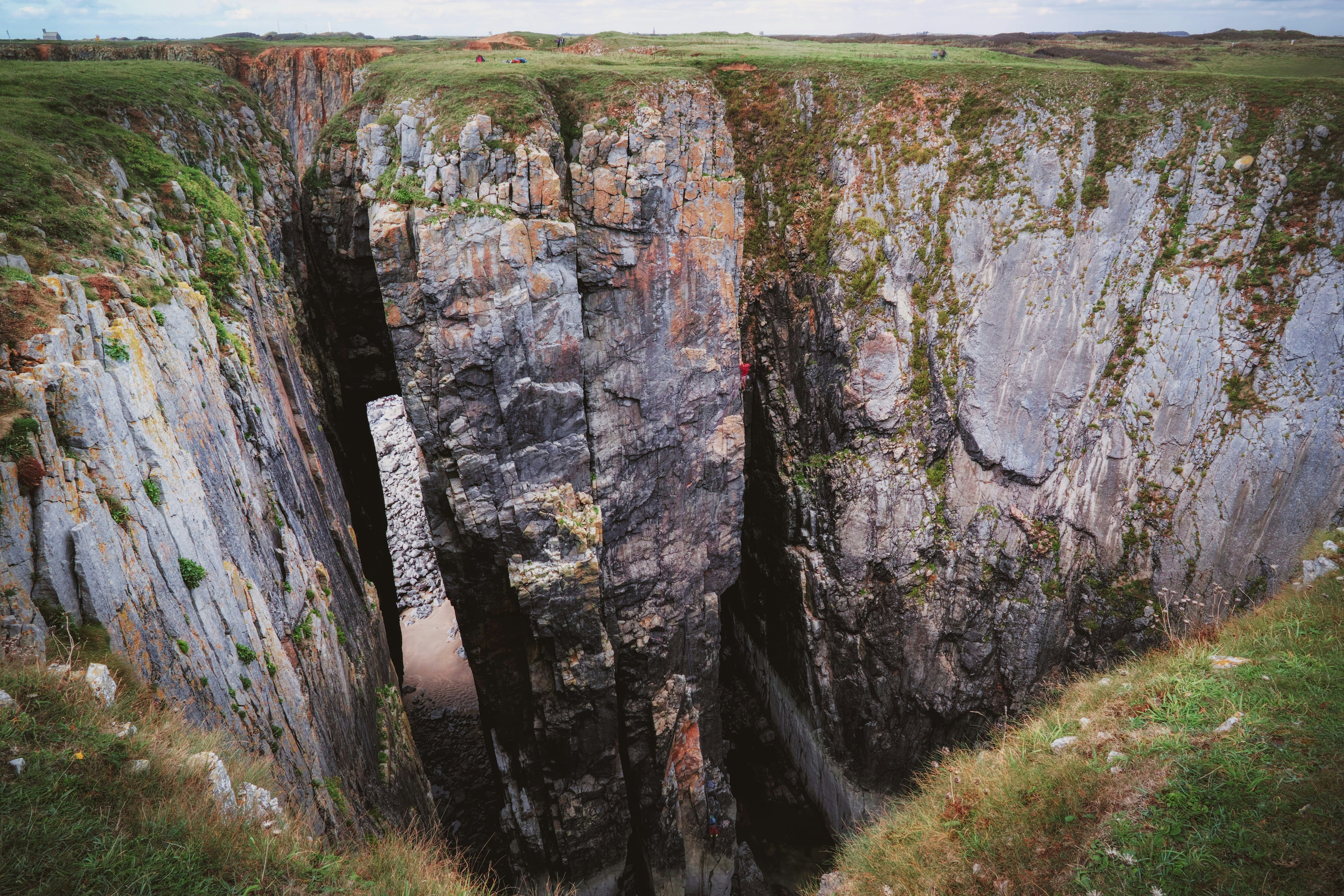 Vertical rock formations create a dramatic chasm leading to a hidden beach below. The rugged textures and colors highlight the power of natural erosion.