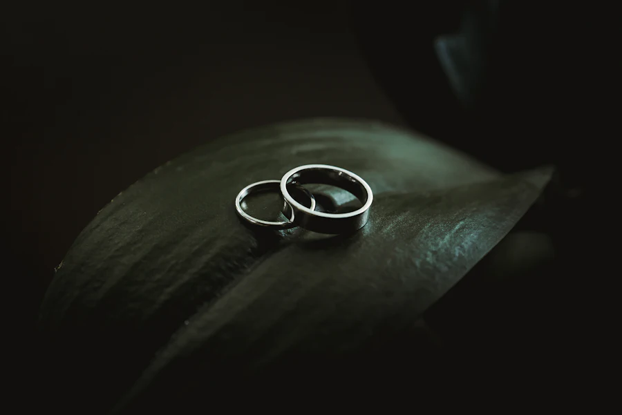 Two silver rings resting on a dark green leaf with moody, low-key lighting and soft reflections.