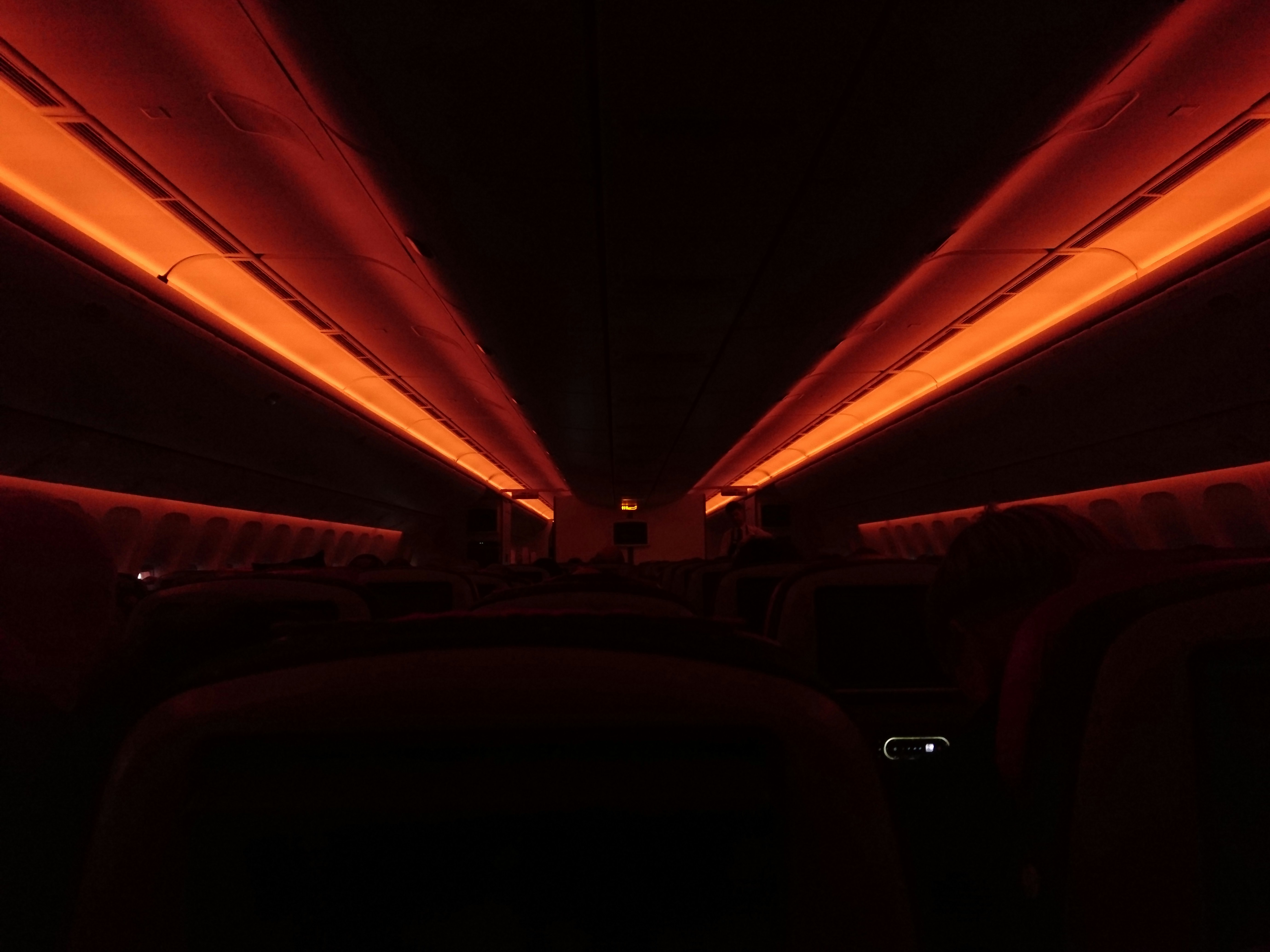 Illuminated airplane cabin bathed in soft red light, showcasing the seating arrangement and ambient glow during a flight.