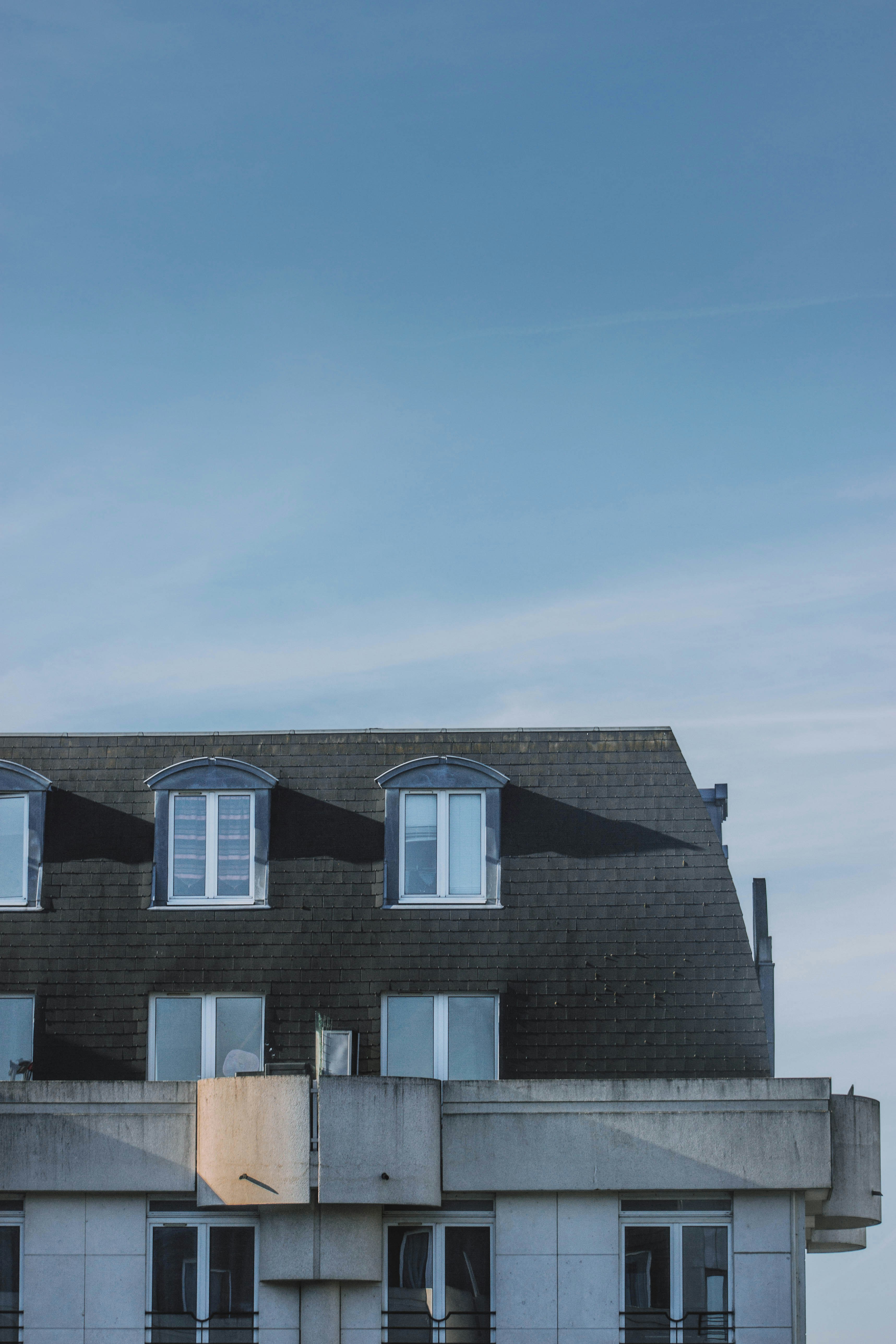 Modern building facade with distinct rooflines and large windows, set against a clear blue sky.