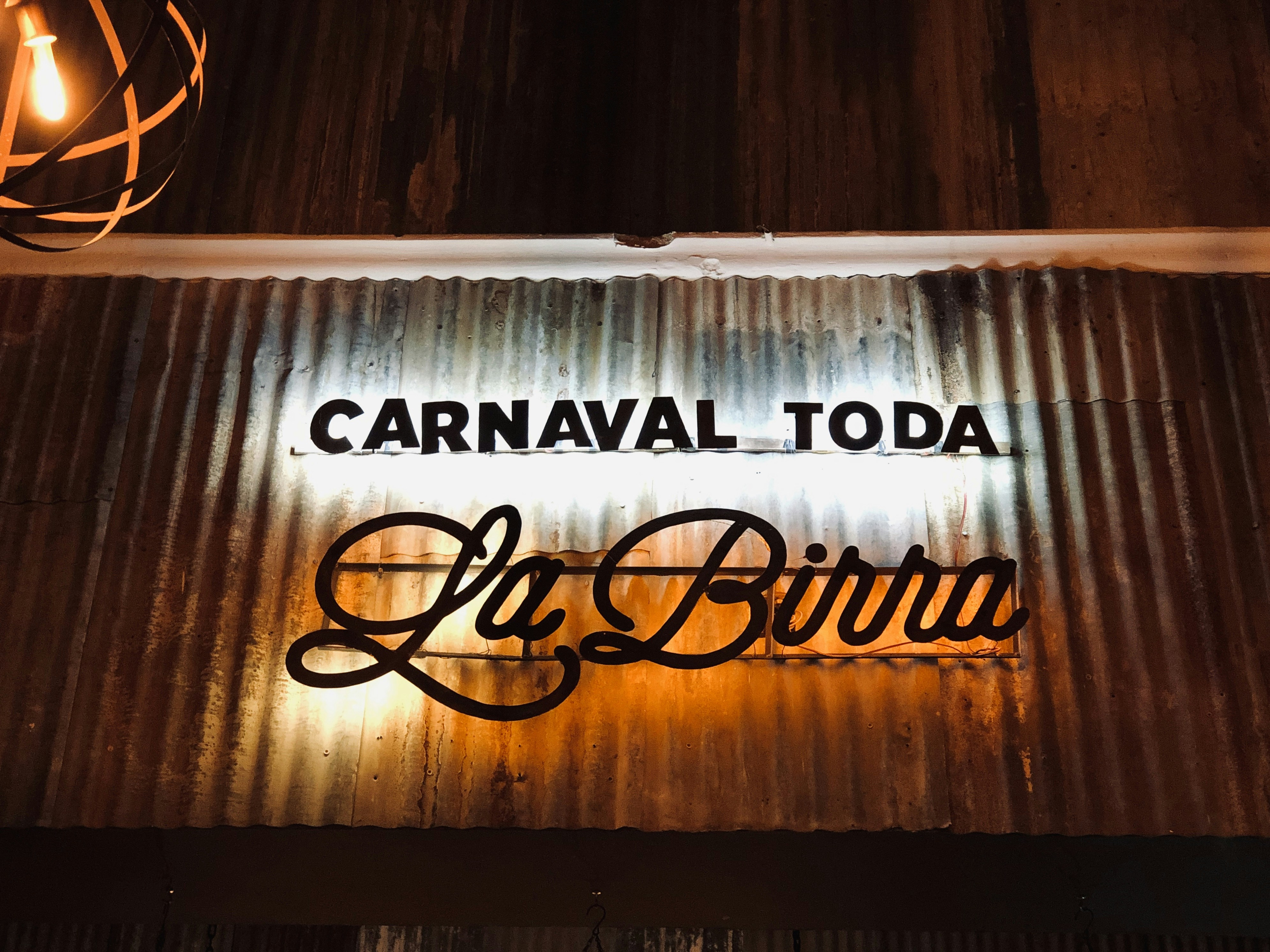 Illuminated sign reading 'Carnaval Toda La Birra' on a textured wall.