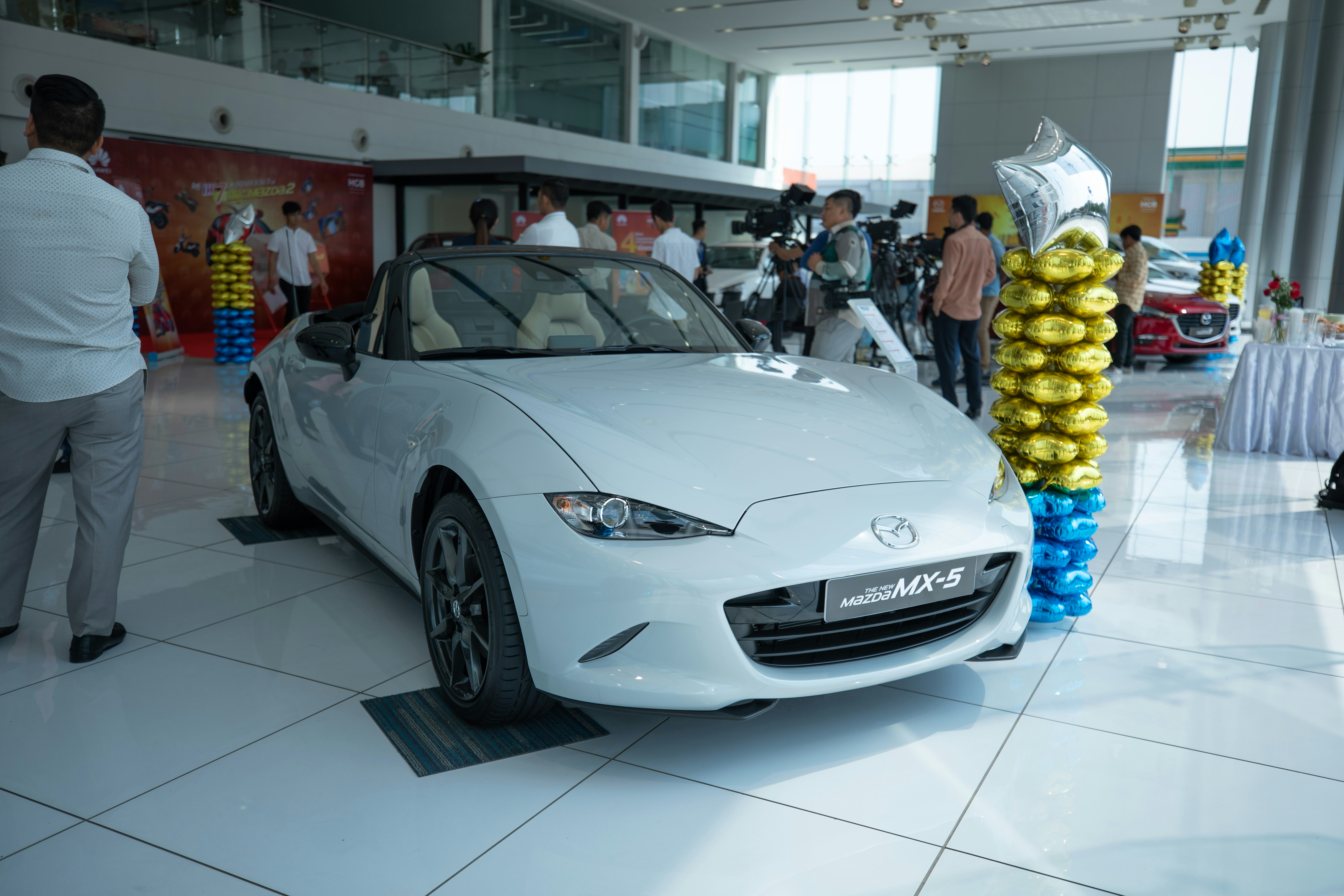 People near white Mazda MX-5 convertible coupe parked inside building ...