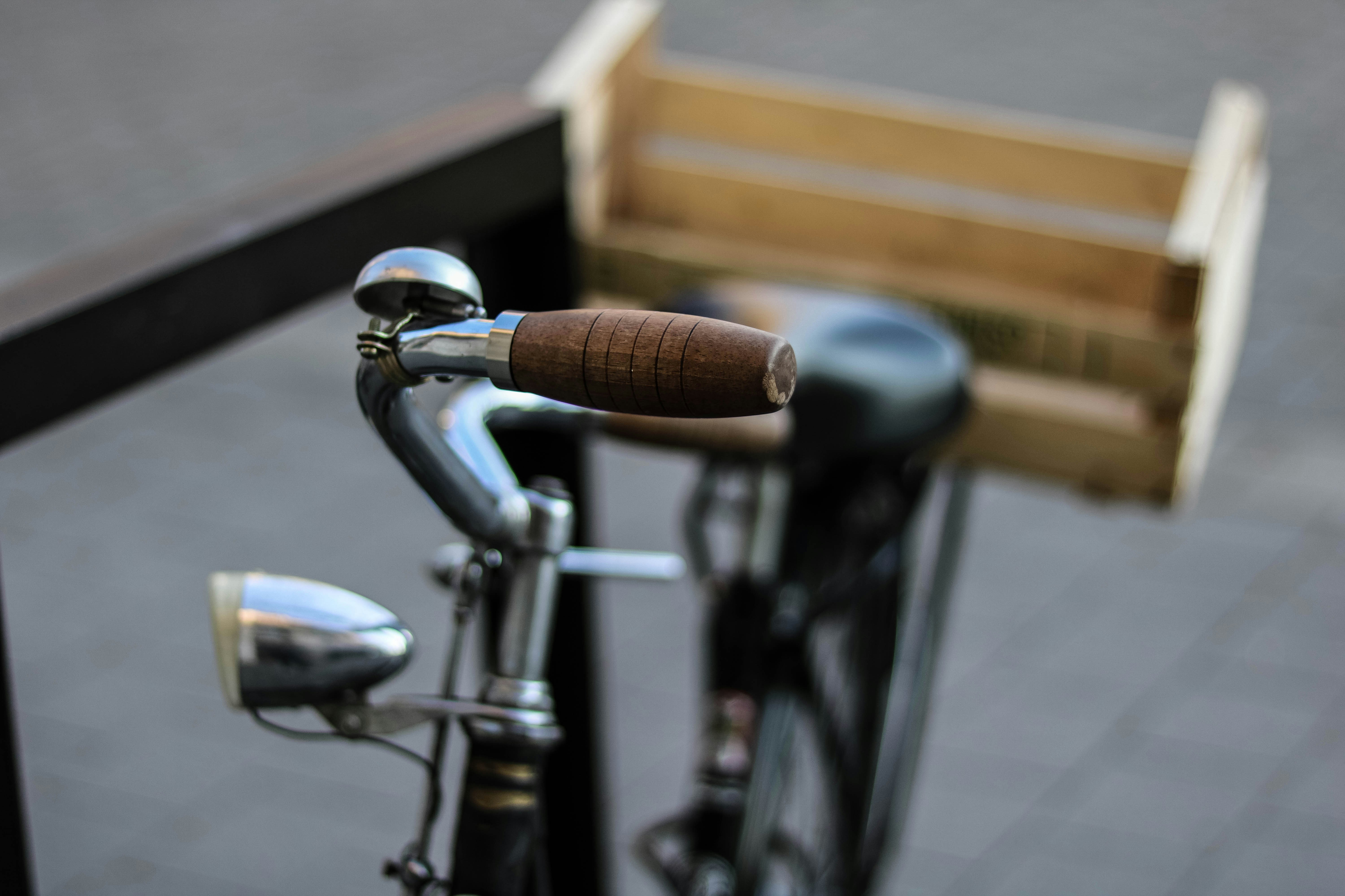 Close-up of a bicycle handlebar with a wooden grip, showcasing the sleek design and reflective chrome details against a blurred background.