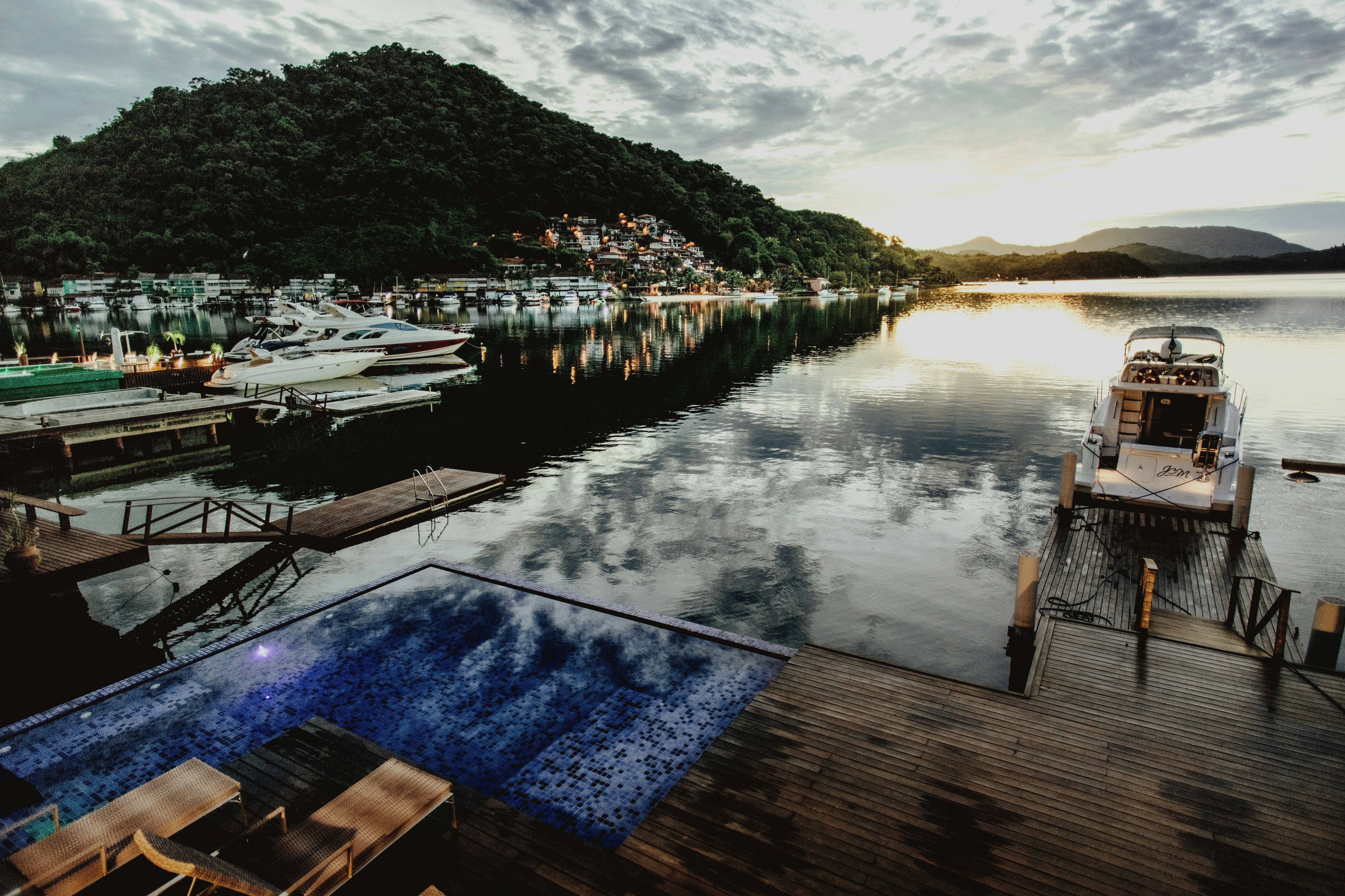 Boats docked at a serene lakeside port with a mountainous backdrop at sunset.