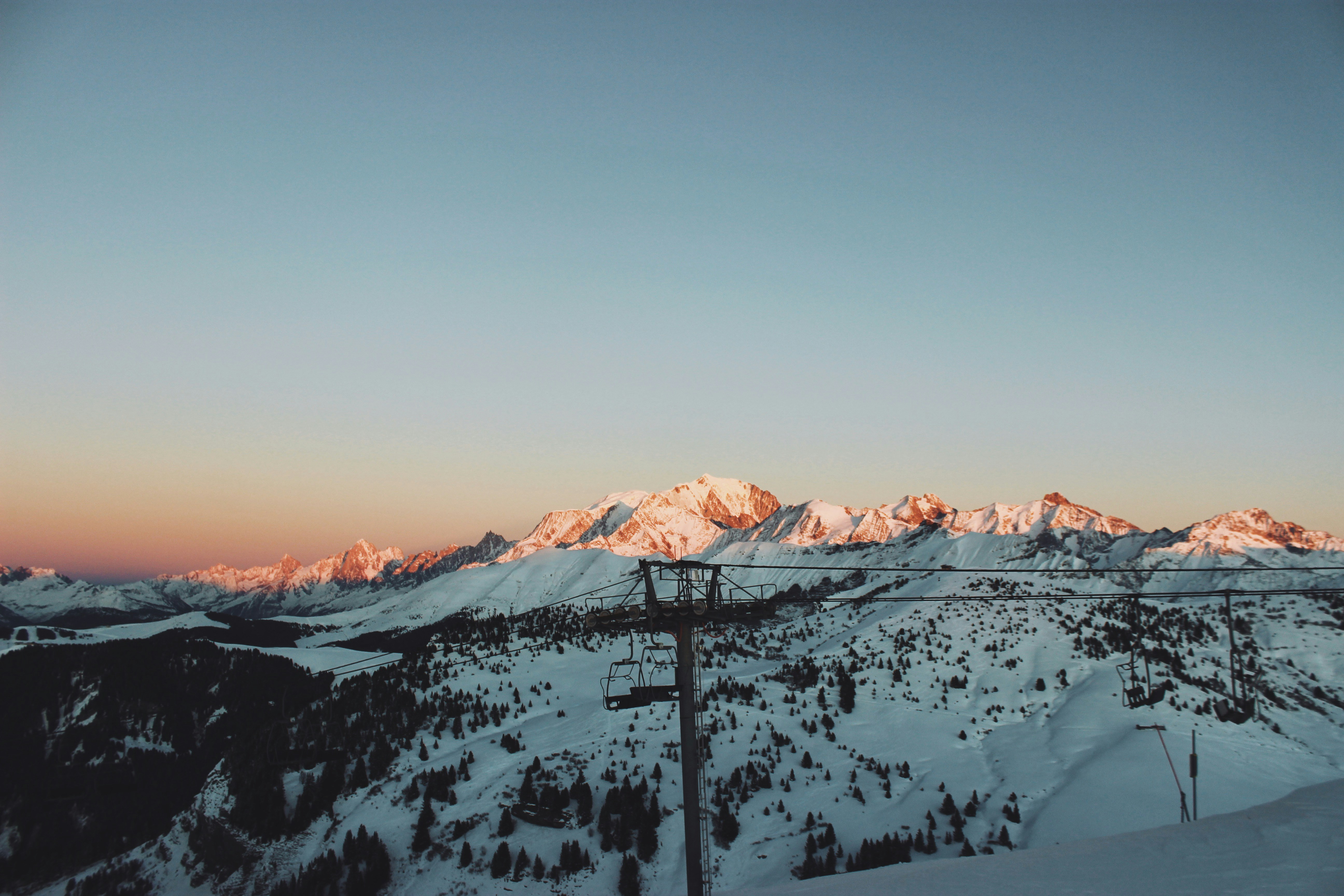 Snow-covered mountains bathed in the soft hues of sunset under a clear sky.