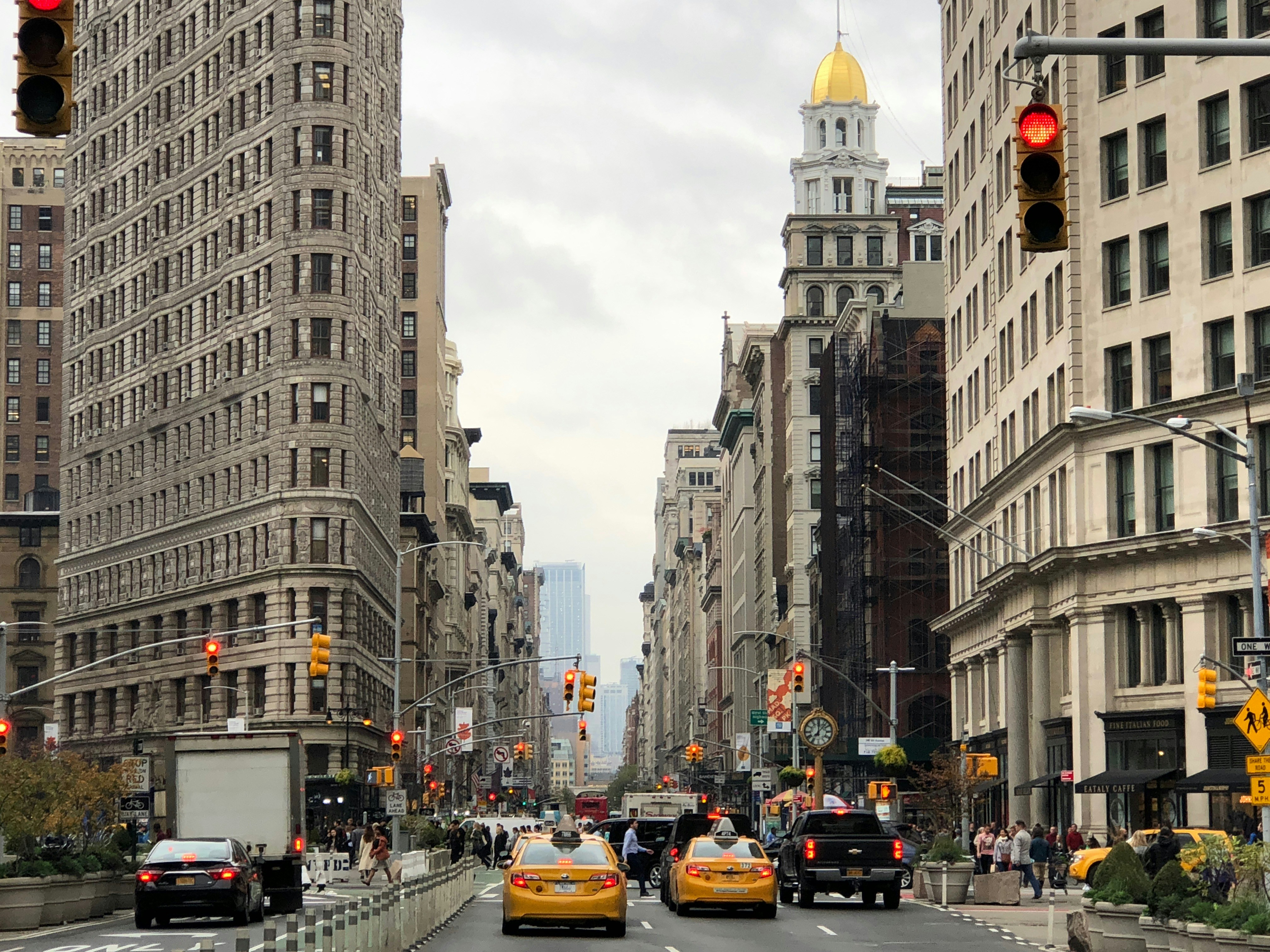 Busy city street lined with historic buildings and yellow taxis, showcasing urban life. Traffic signals and pedestrians add to the dynamic atmosphere.