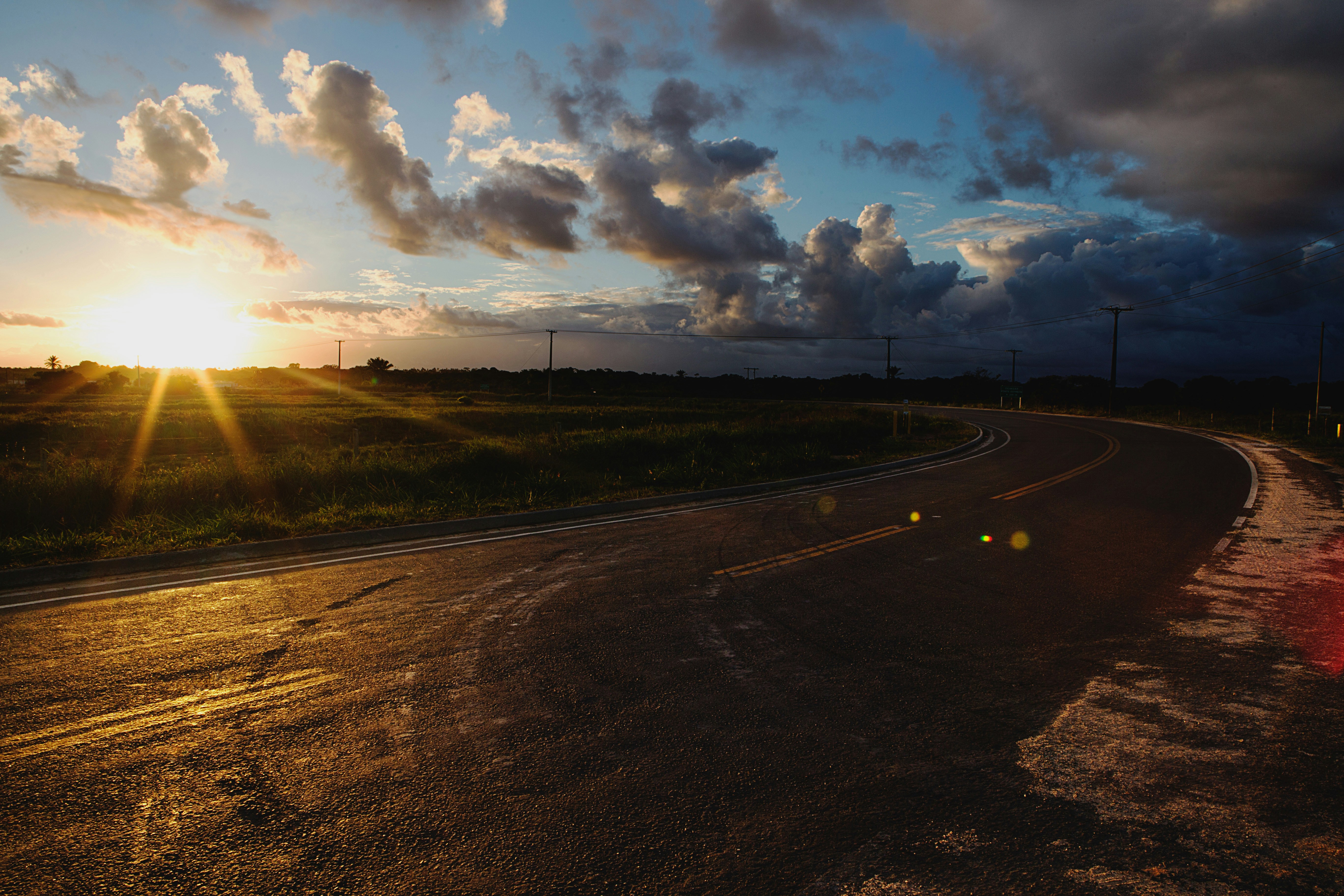 Curving road under a vibrant sunset, with clouds reflecting warm hues. The scene captures the tranquil transition from day to night.
