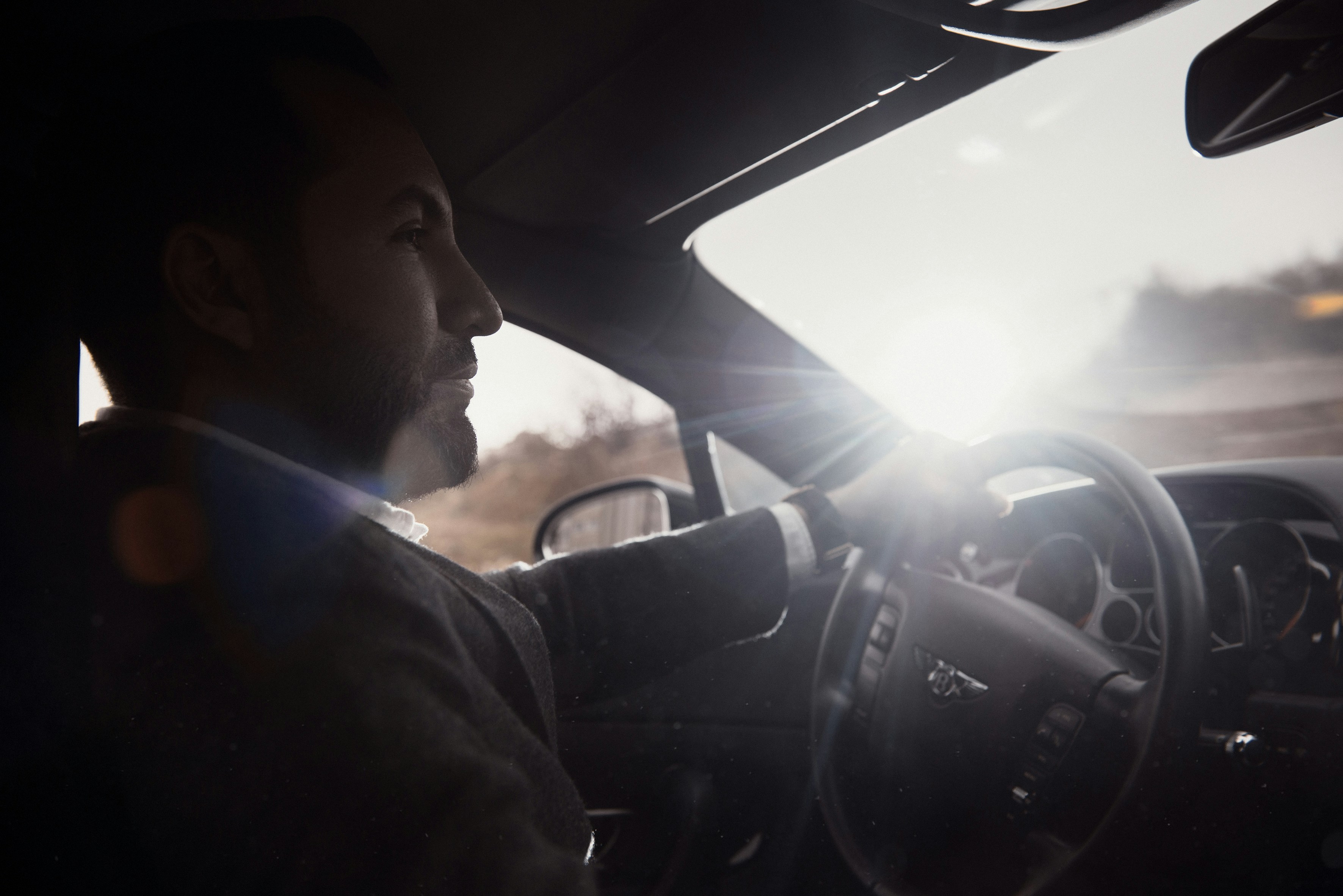 Driver in silhouette with sunlight streaming through the car window, highlighting the steering wheel and dashboard.