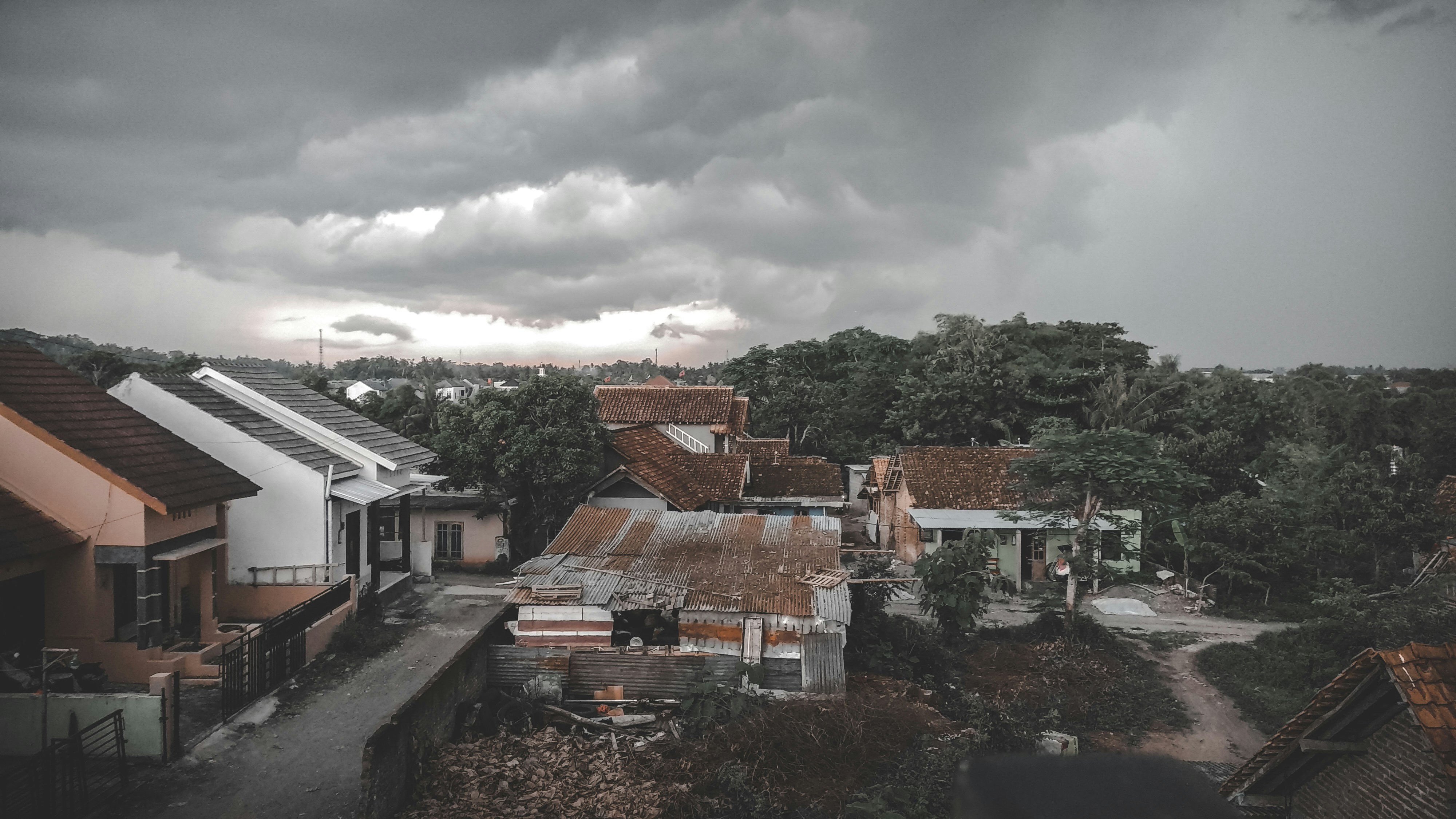 Aerial view of a tranquil suburban landscape under a dramatic overcast sky, featuring a mix of traditional and modern architecture.