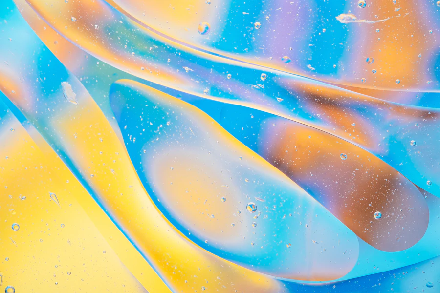 Glossy abstract swirls of cyan, yellow, and orange with floating bubble-like droplets. Smooth translucent shapes overlap in a bright, luminous composition.