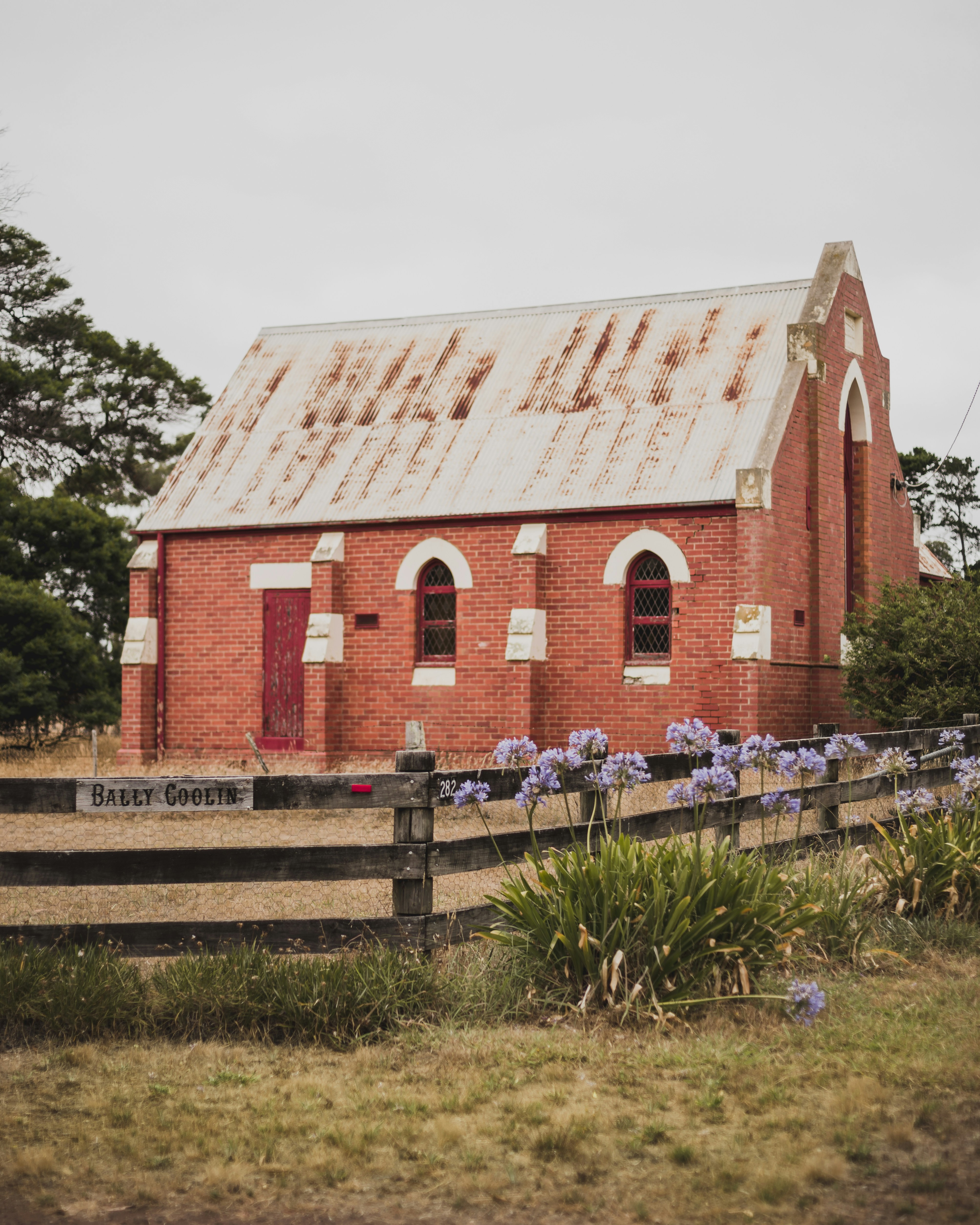 Red-brick chapel under a weathered tin roof, framed by a lavender-bordered fence