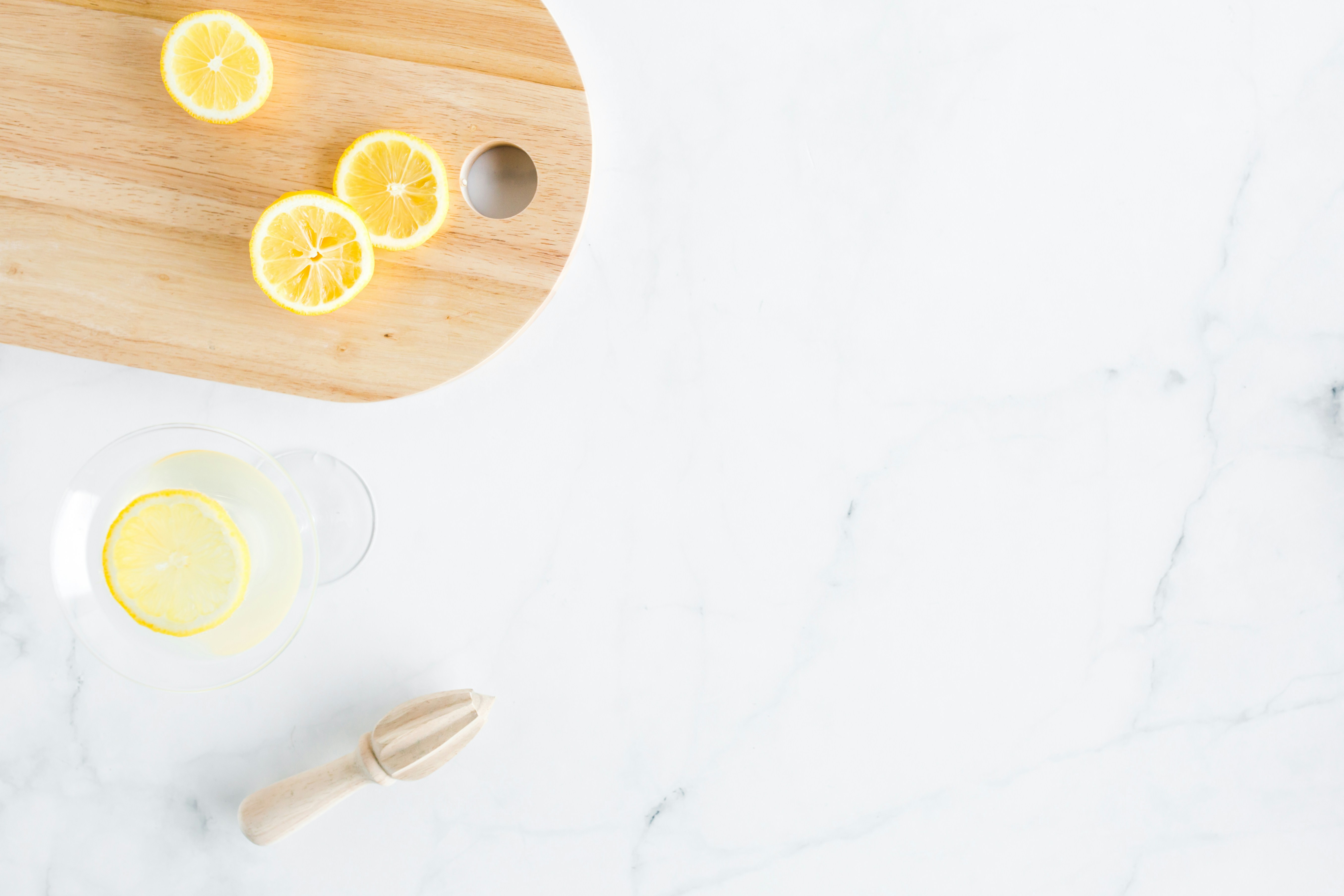 Sliced lemons on a wooden board beside a juicer on a marble surface.