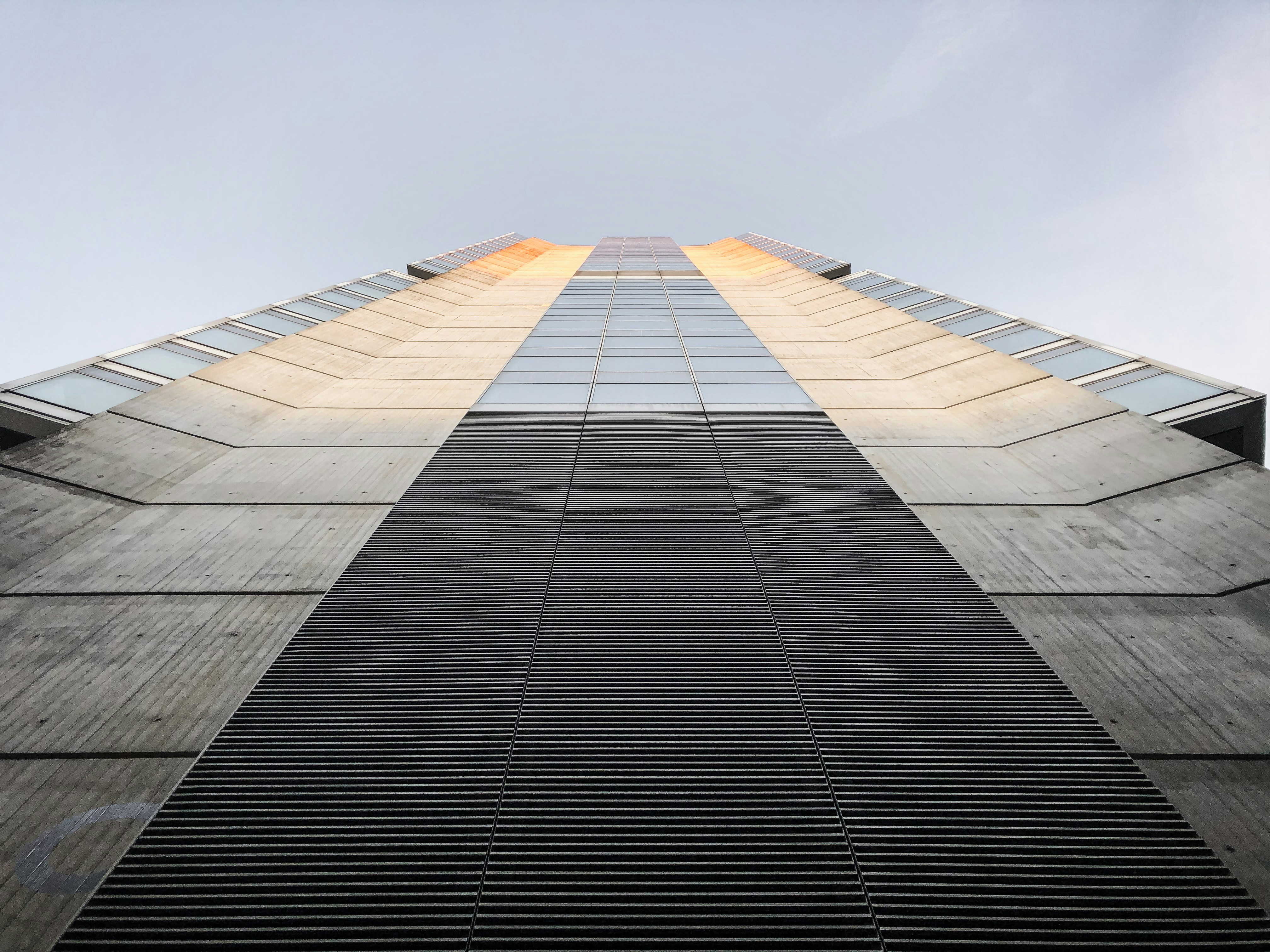 Low-angle view of a modern concrete building with symmetrical lines reaching into a cloudy sky.