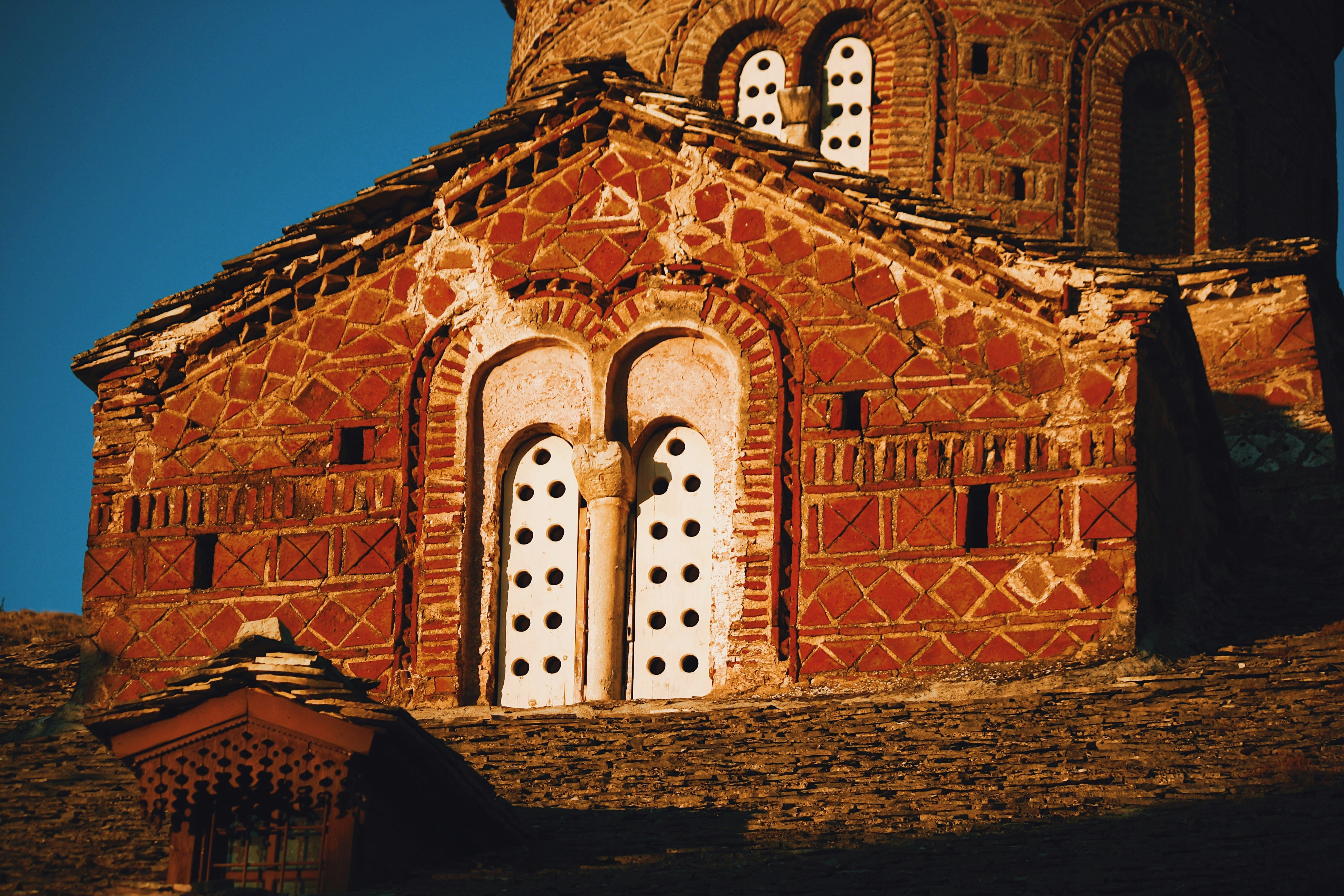 Intricate brickwork and distinctive windows of an ancient structure bathed in warm sunlight.