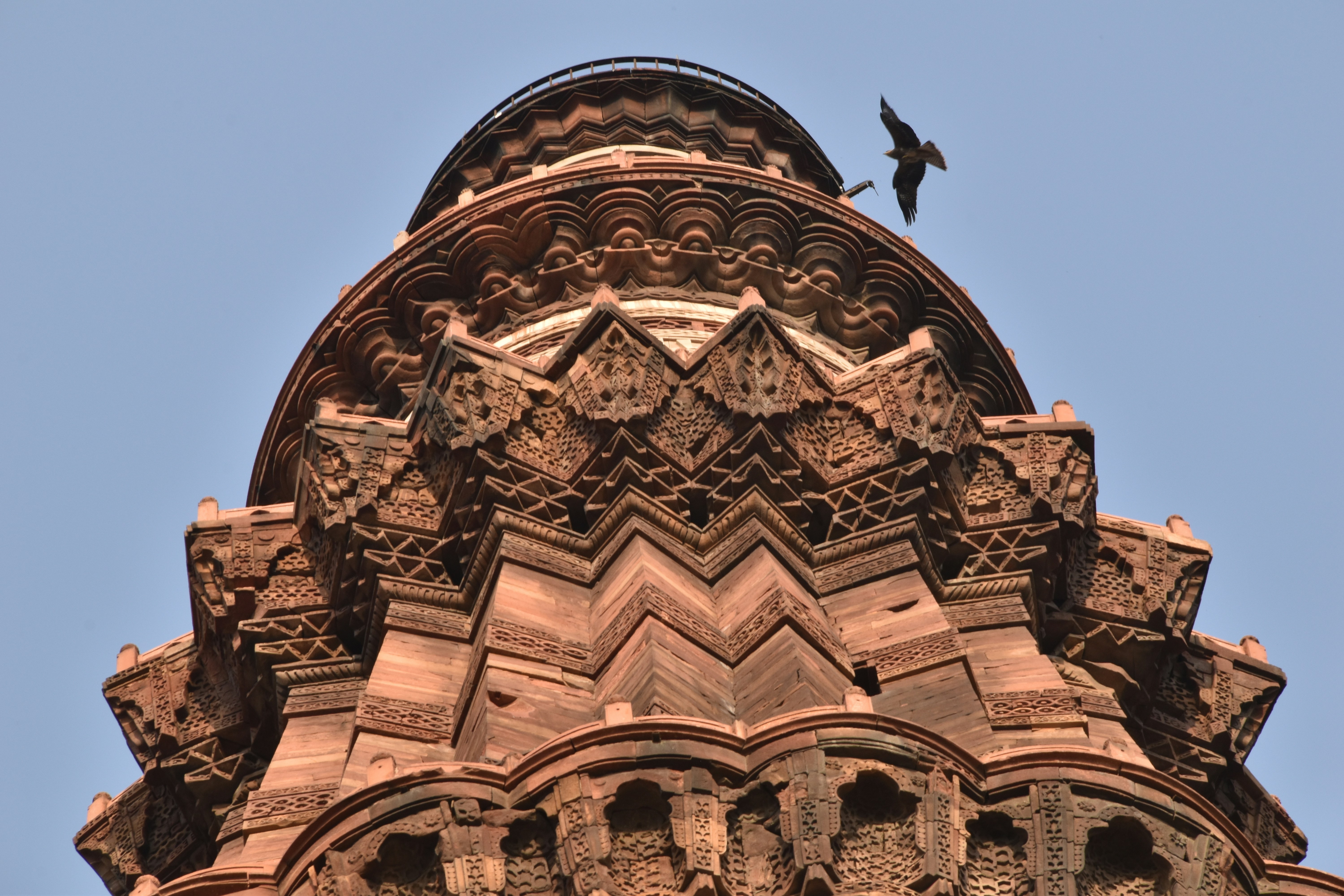 Intricate architectural details of a historical tower with a bird soaring above against a clear blue sky.