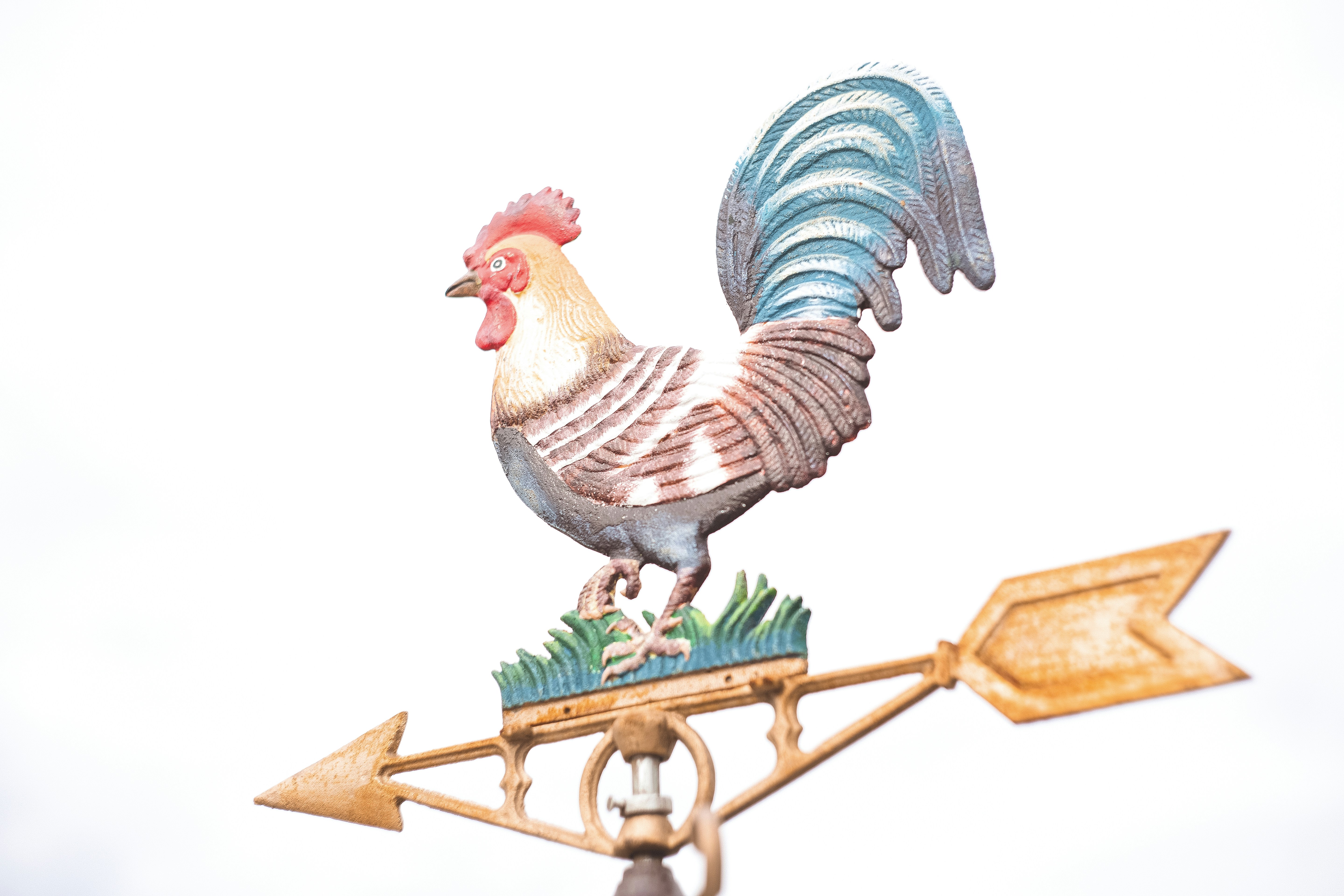 Colorful rooster weather vane atop a rustic structure, showcasing intricate detailing against a bright sky.