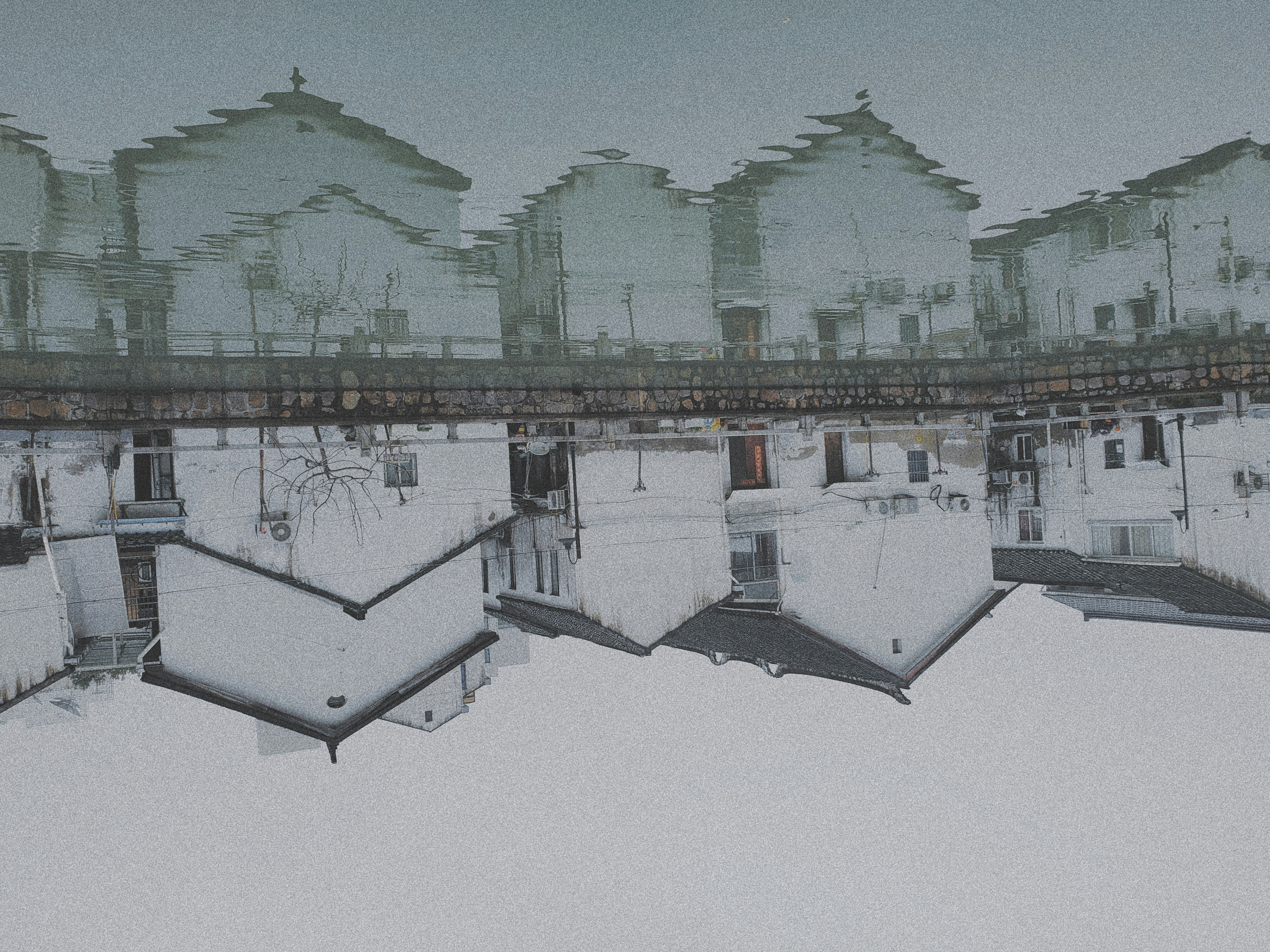 Snow-covered houses reflected in a serene, icy surface.