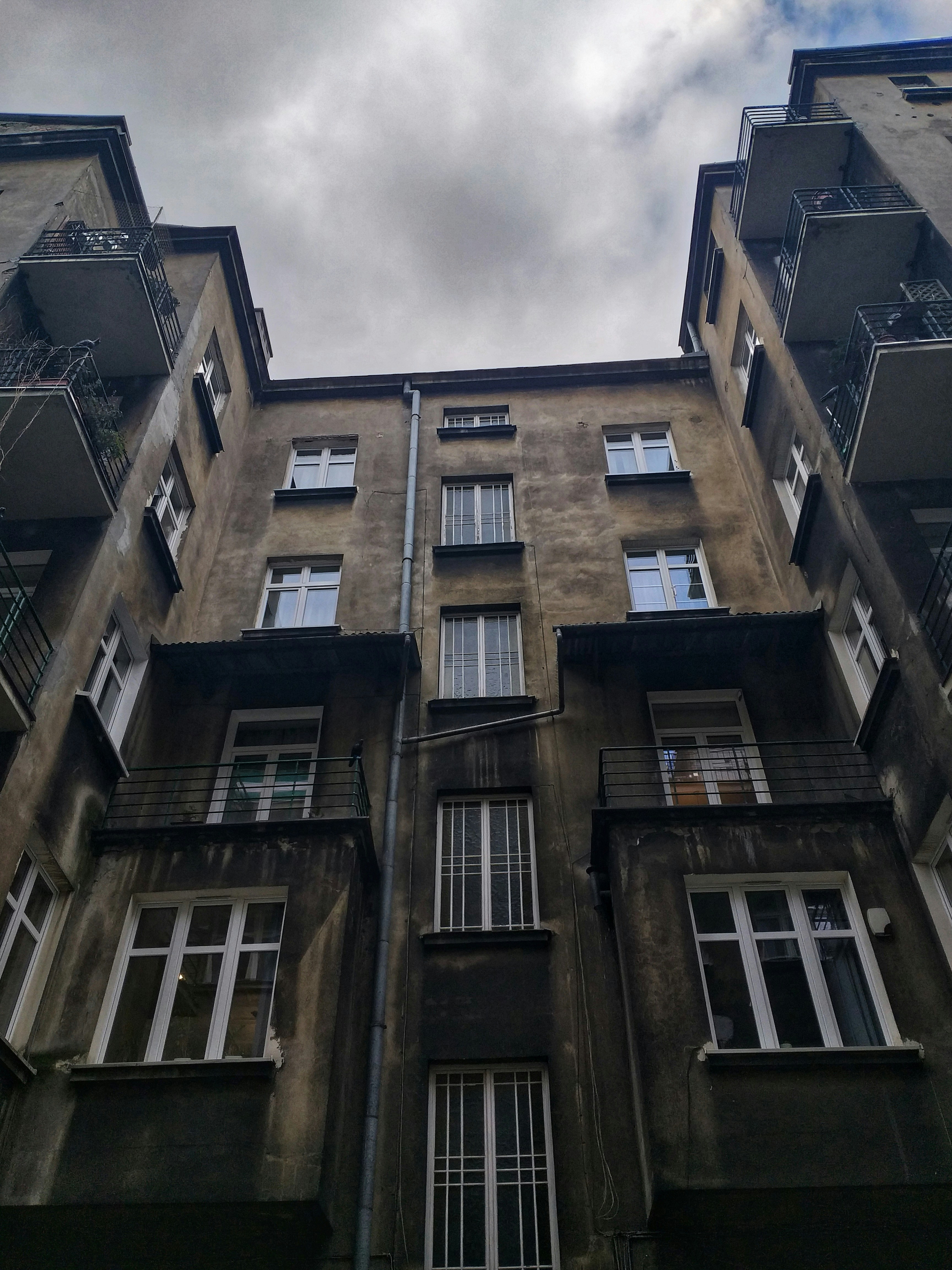 View of a narrow courtyard framed by weathered apartment buildings, showcasing a mix of architectural styles and cloudy skies above.