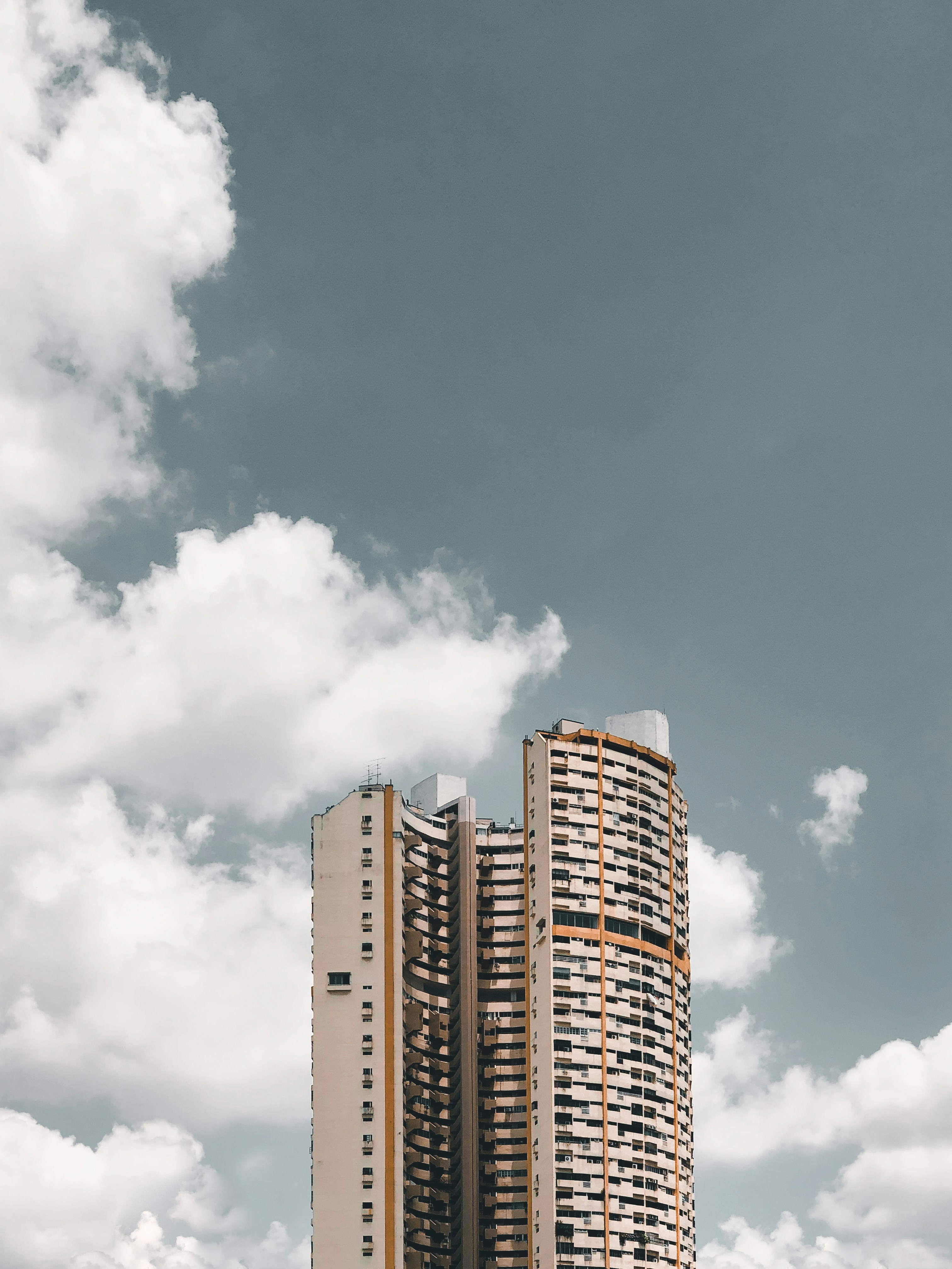 Tall residential building rising amidst a backdrop of fluffy clouds and a clear sky.