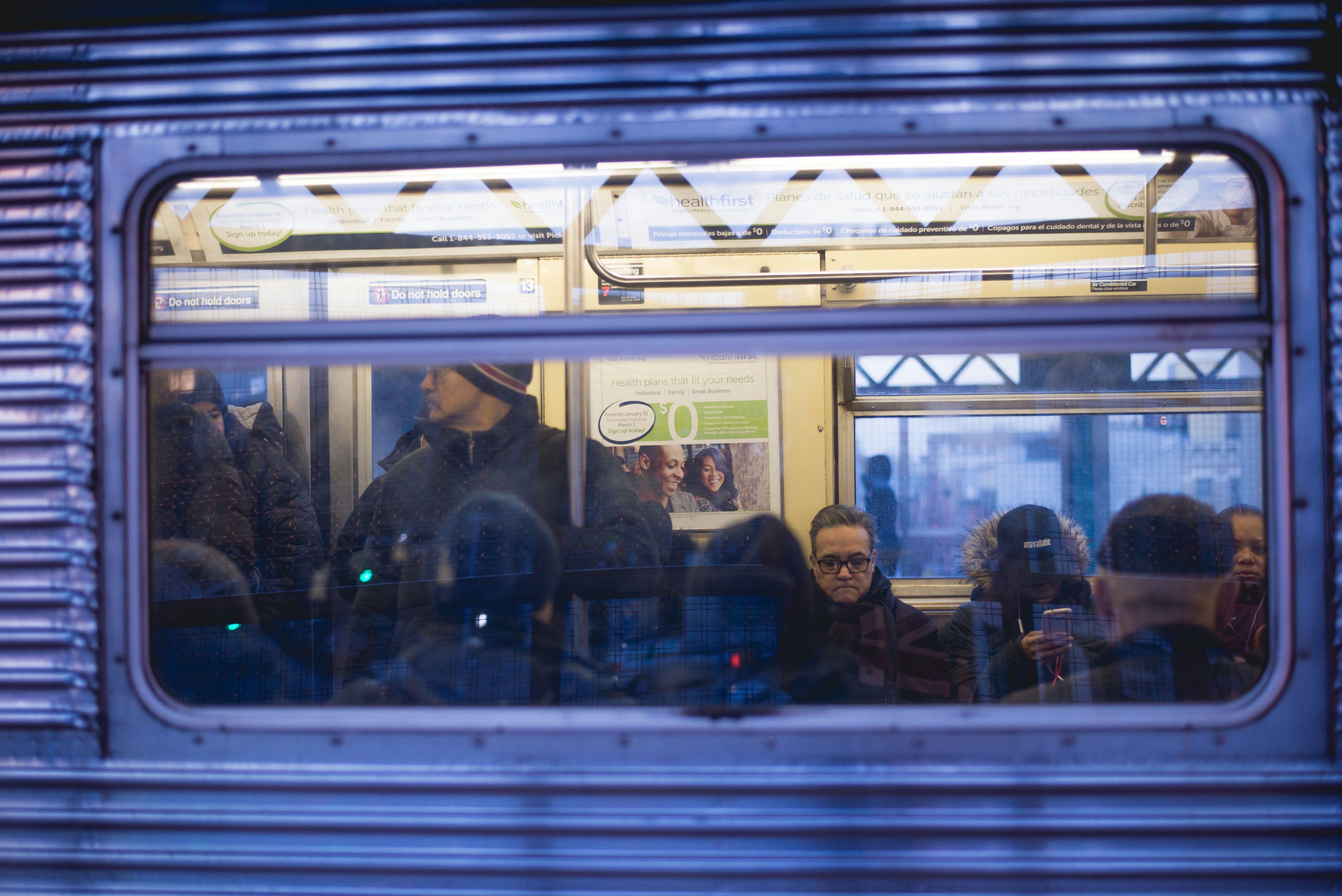 Passengers in a subway train captured through a window, showcasing the everyday hustle of city commuting.