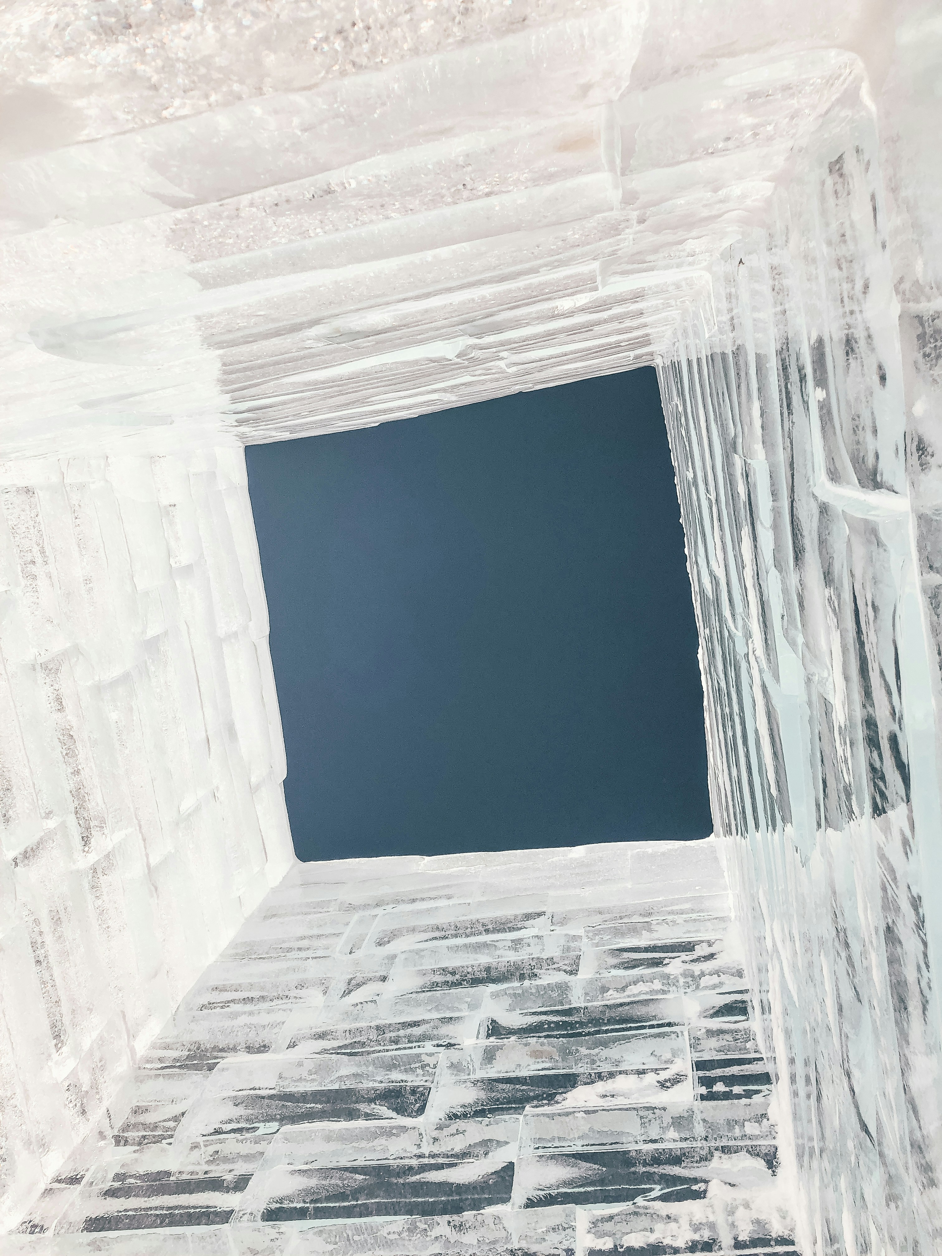 Looking up through a transparent ice structure towards a clear blue sky.