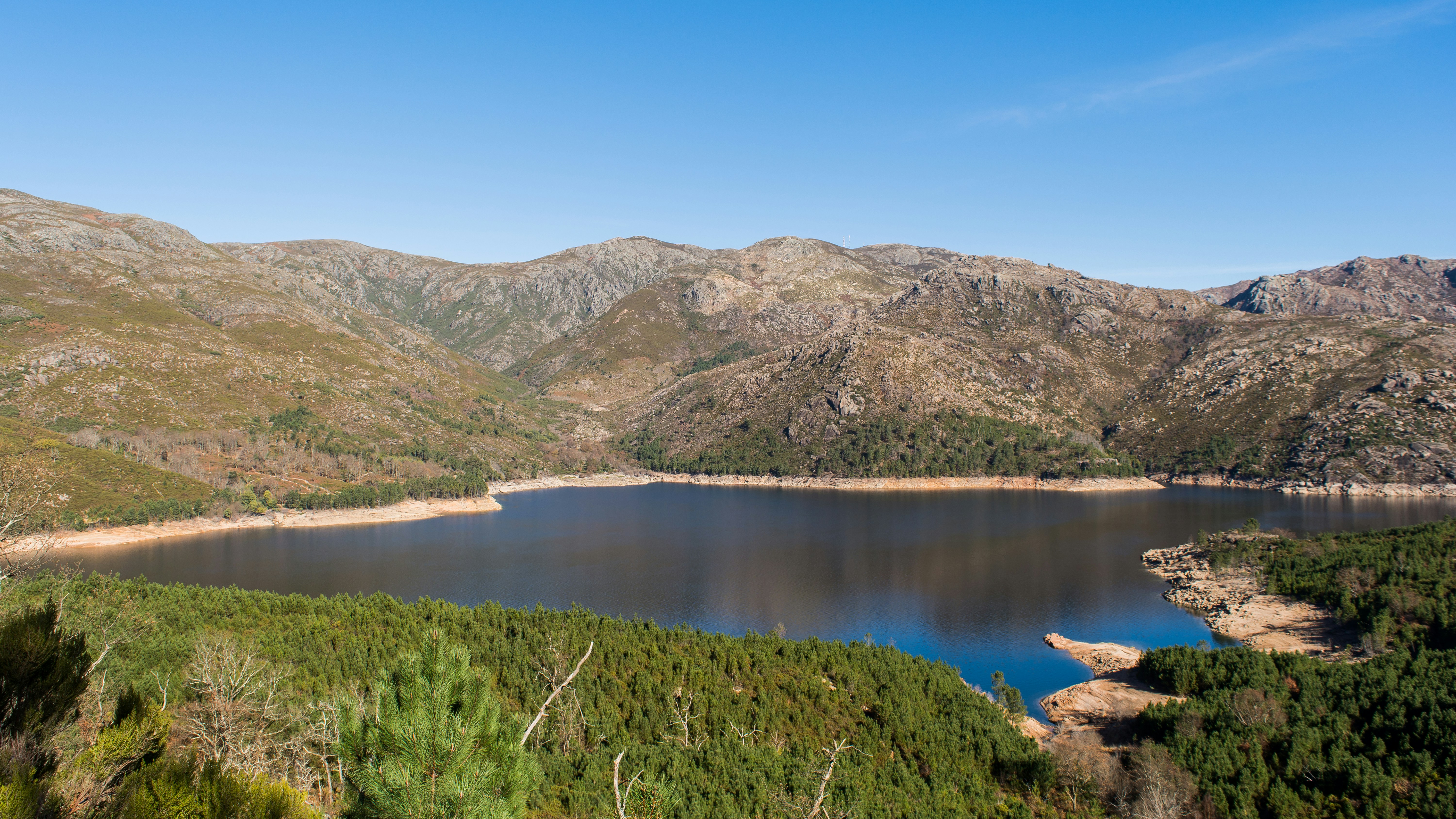 Tranquil lake nestled between rolling hills under a clear blue sky.