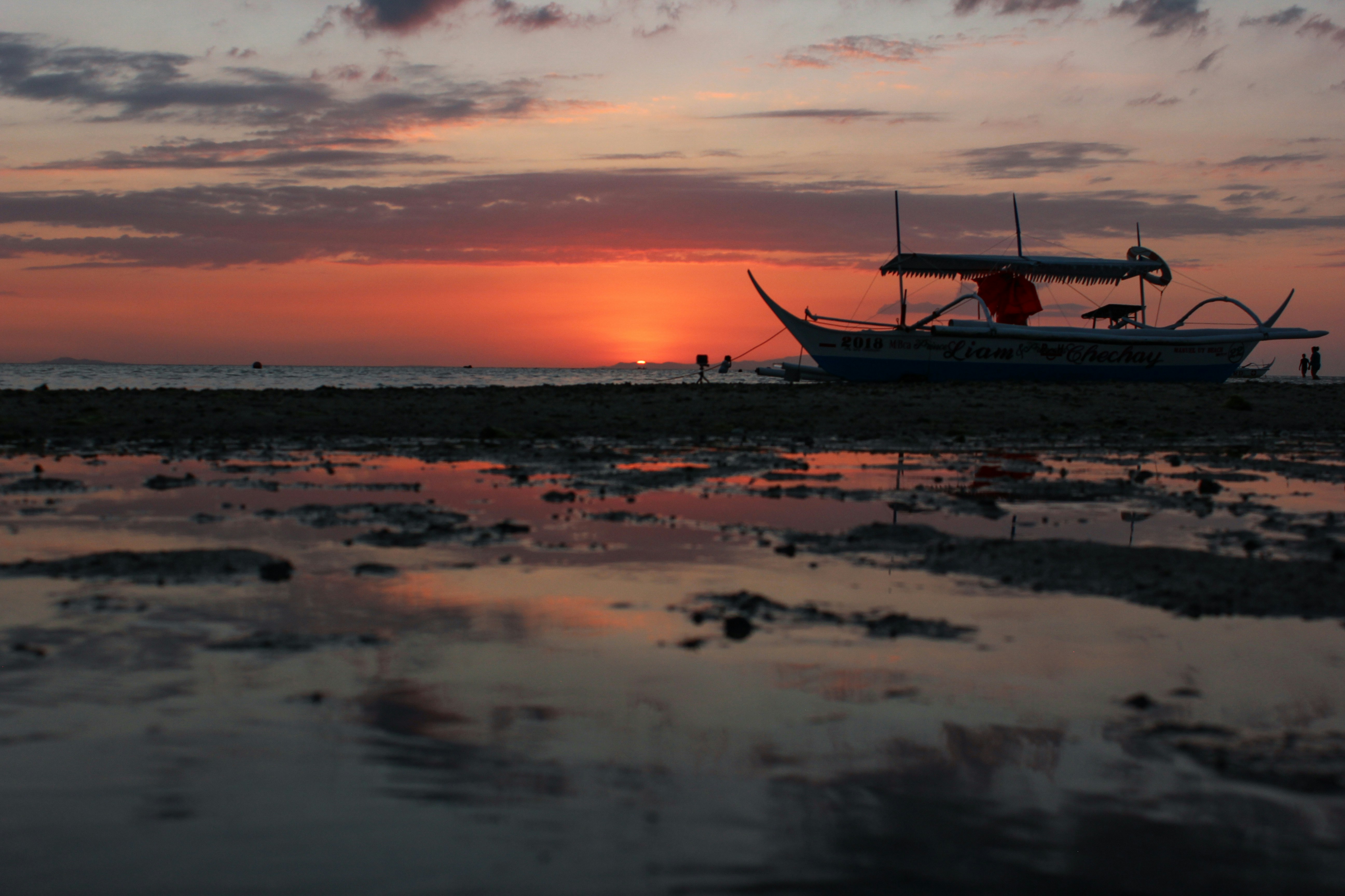 Fishing boat anchored on a tranquil shore, reflecting the vibrant hues of sunset over the calm sea.