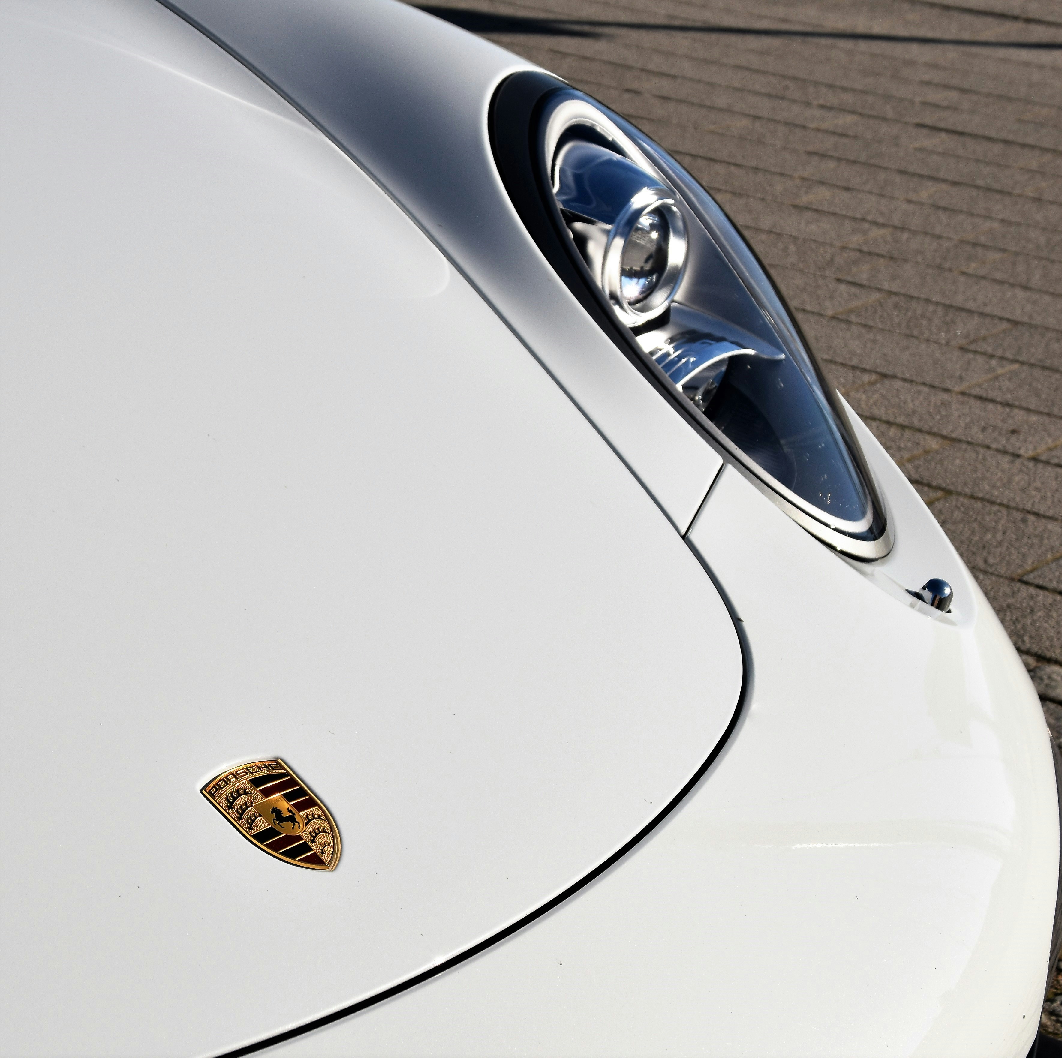 Close-up of a Porsche emblem on a sleek white car hood, showcasing the vehicle's refined aesthetics and craftsmanship.