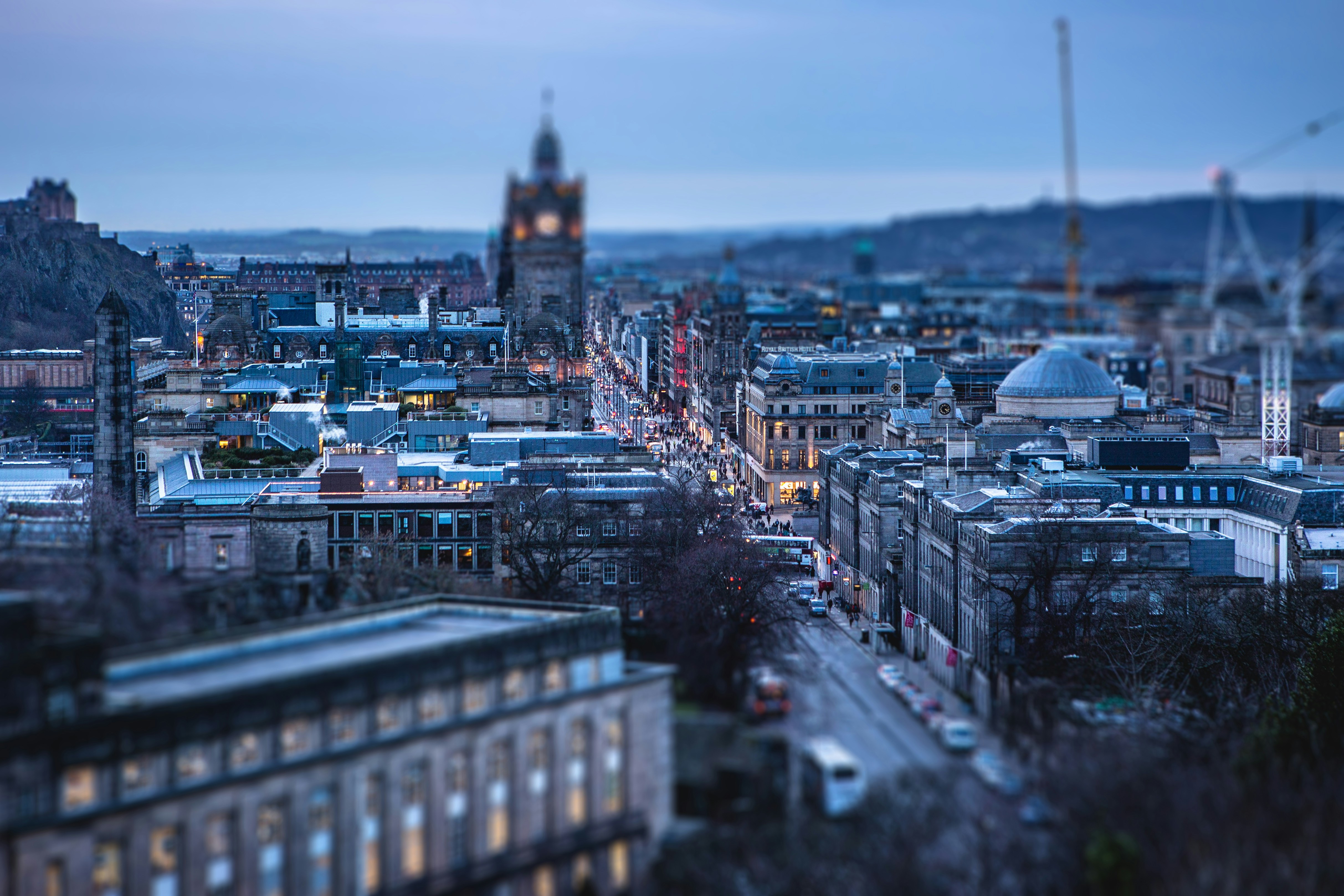 Aerial view of Edinburgh at dusk, showcasing the city's iconic architecture and bustling streets illuminated by soft evening light.