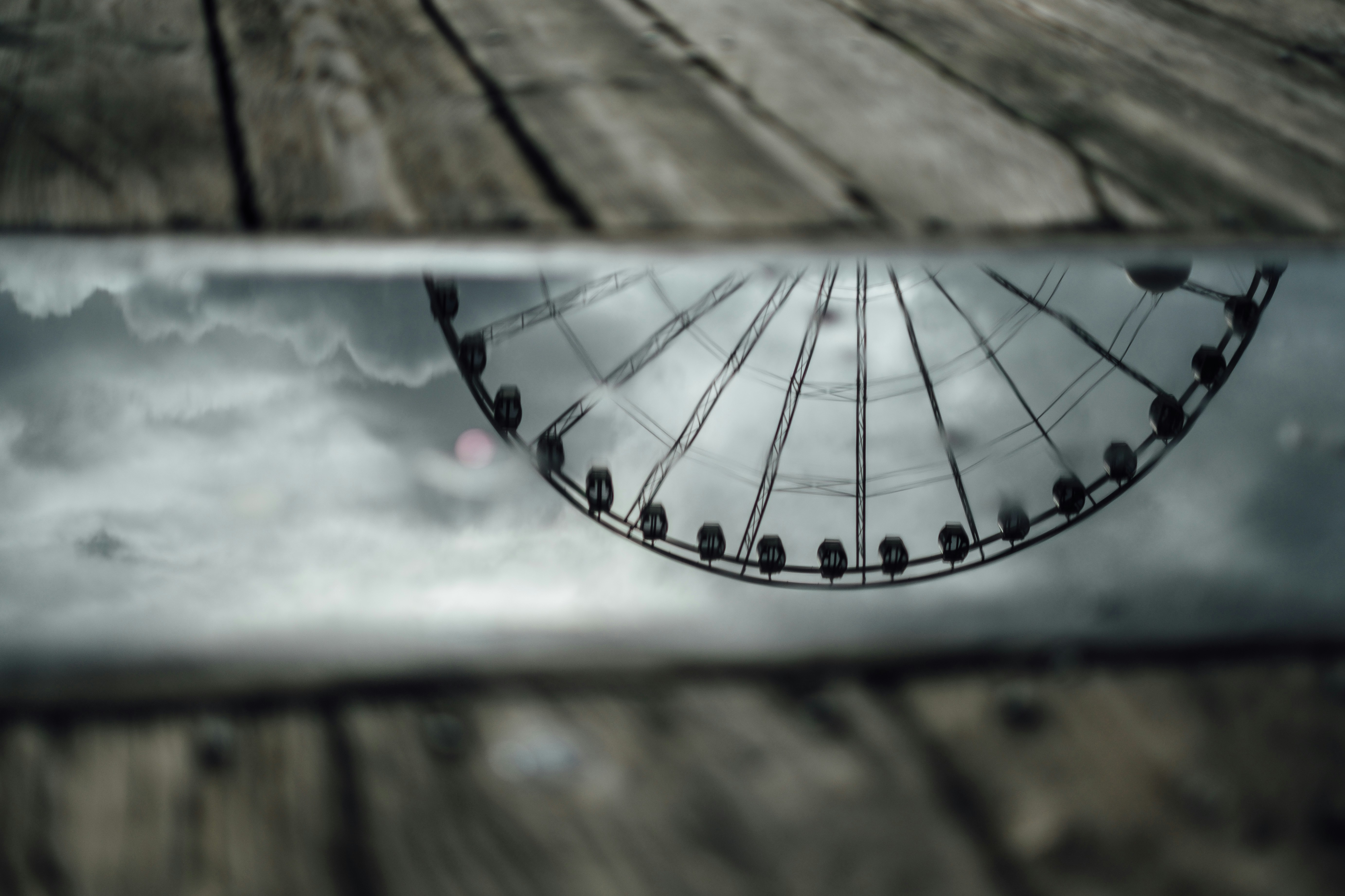 Reflection of a Ferris wheel in a puddle on weathered wooden planks, capturing a moody atmosphere.