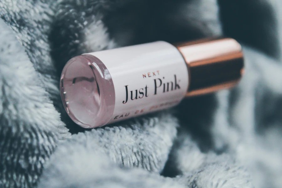 A small pink perfume bottle labeled “Next Just Pink” rests on a plush gray blanket, with a rose-gold cap catching the light.
