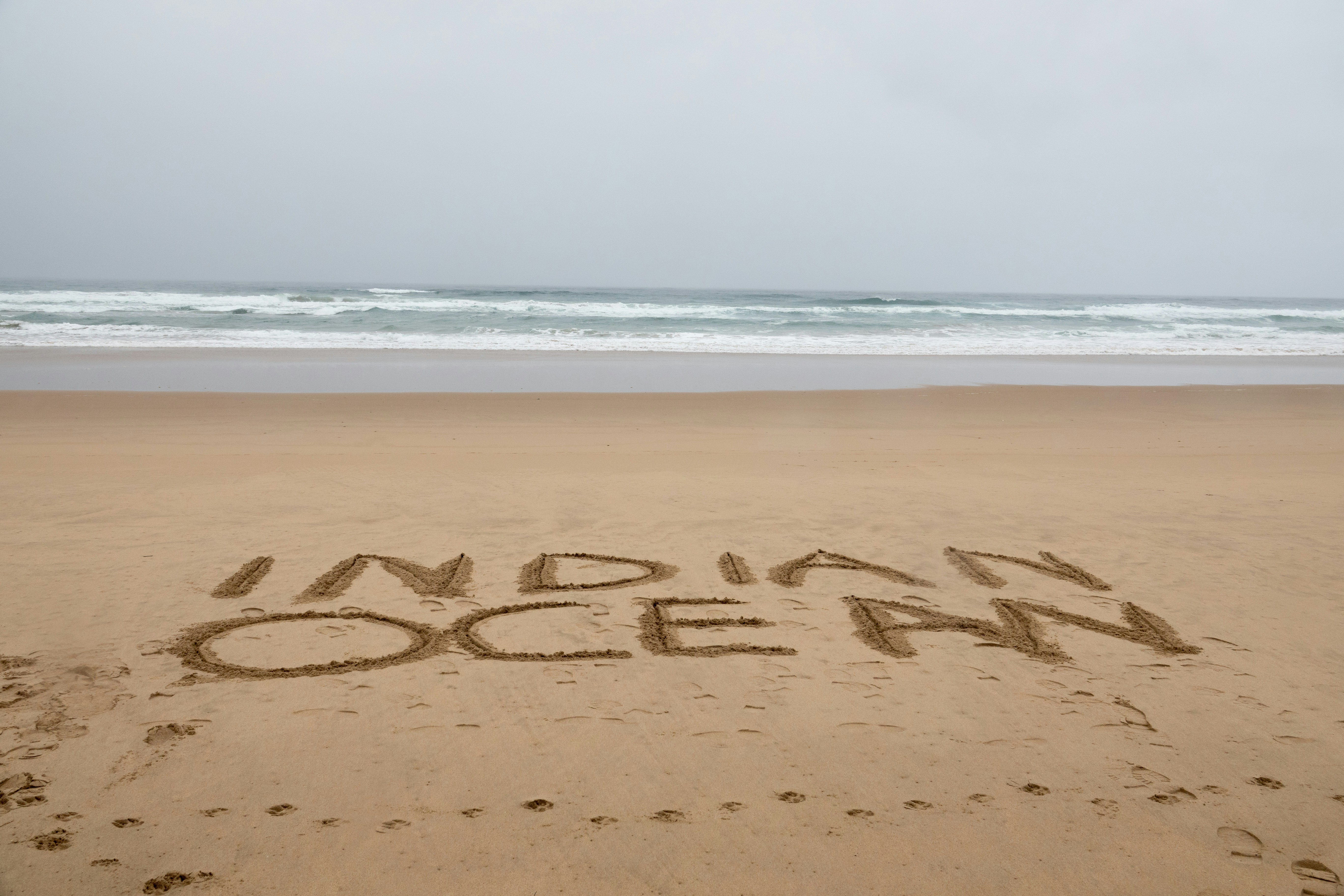Words 'Indian Ocean' etched into wet sand with waves in the background.