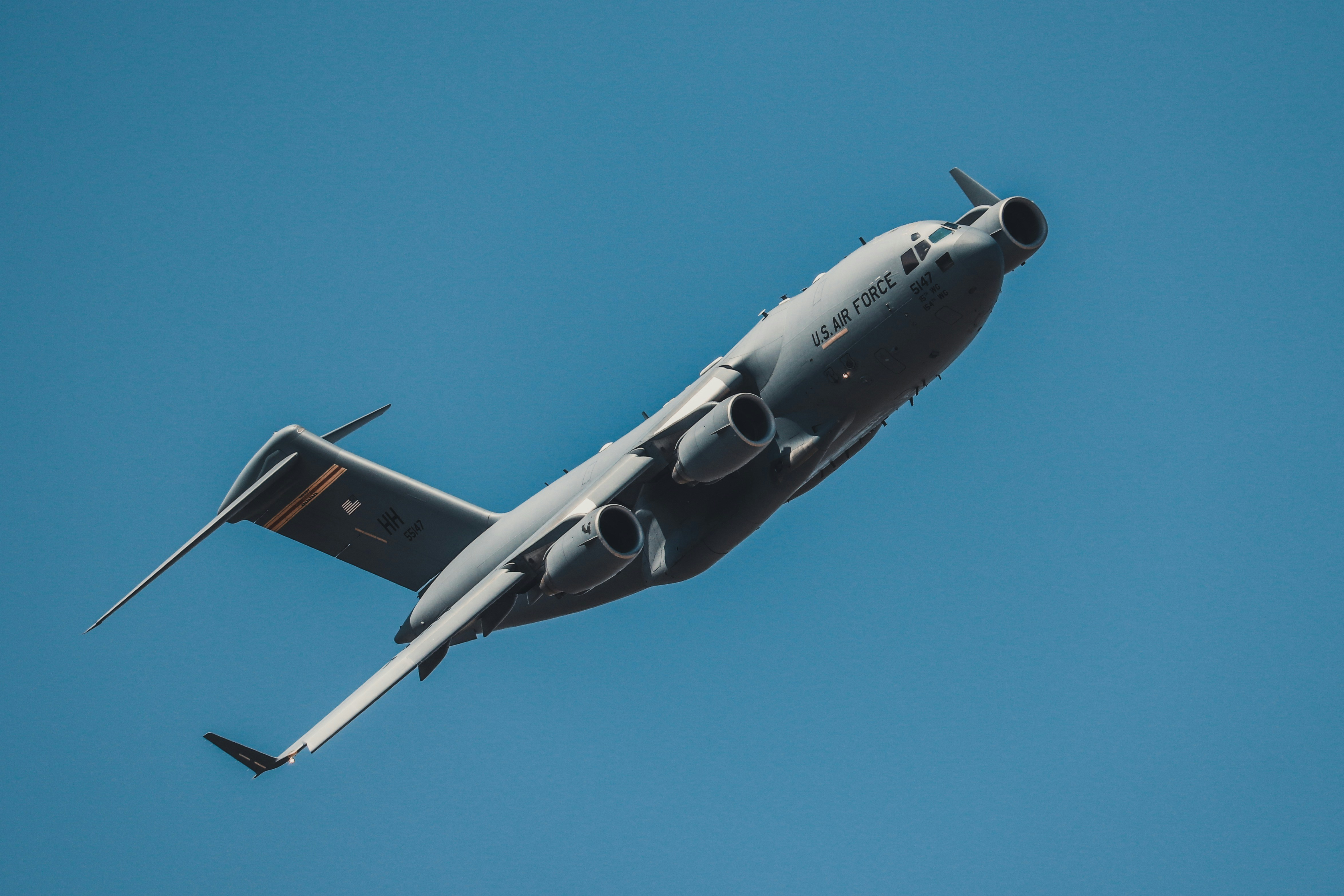 Military cargo aircraft performing a steep climb against a clear blue sky.