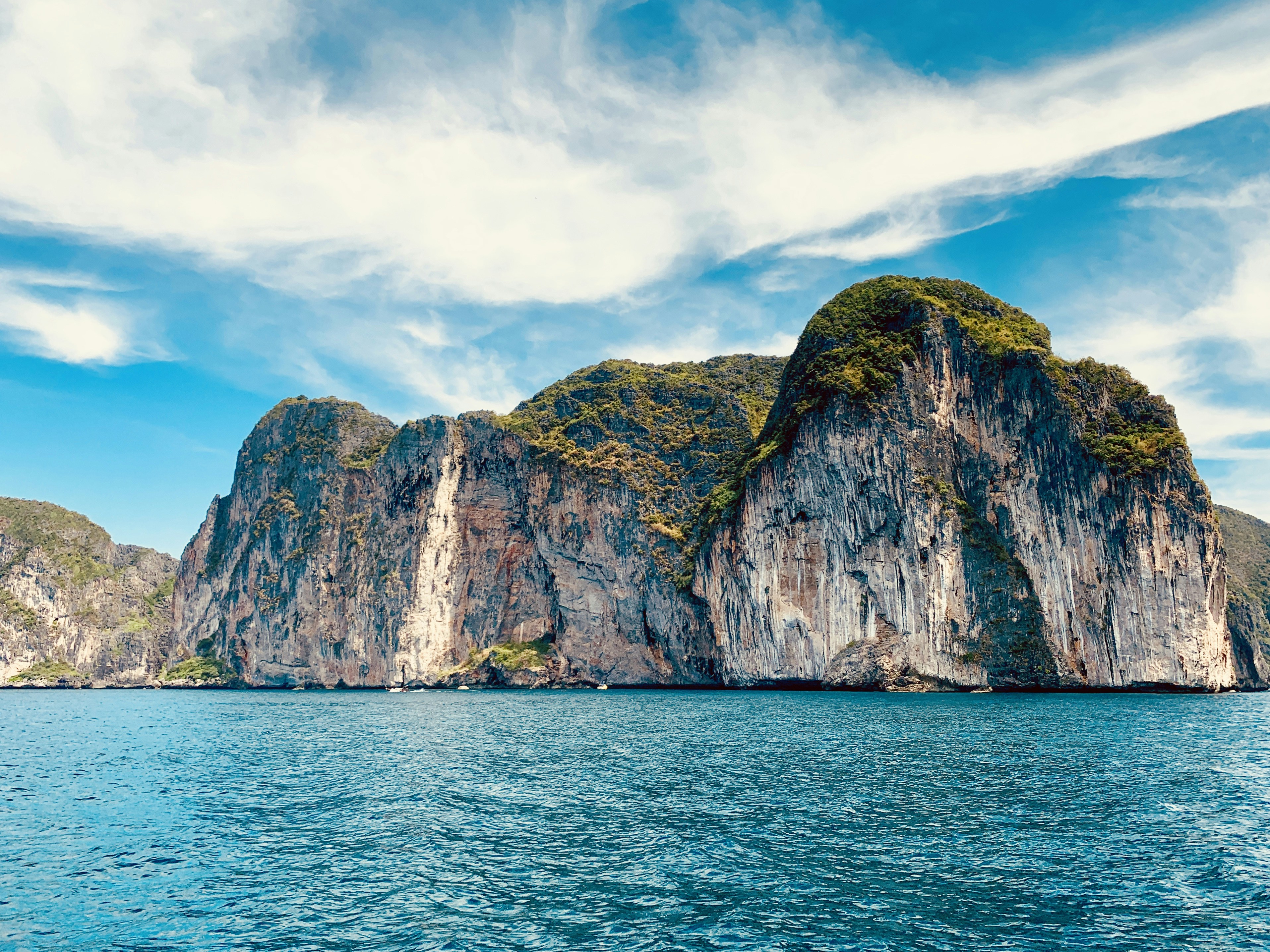 Towering cliffs rise dramatically from the turquoise waters, adorned with lush greenery under a vibrant sky.