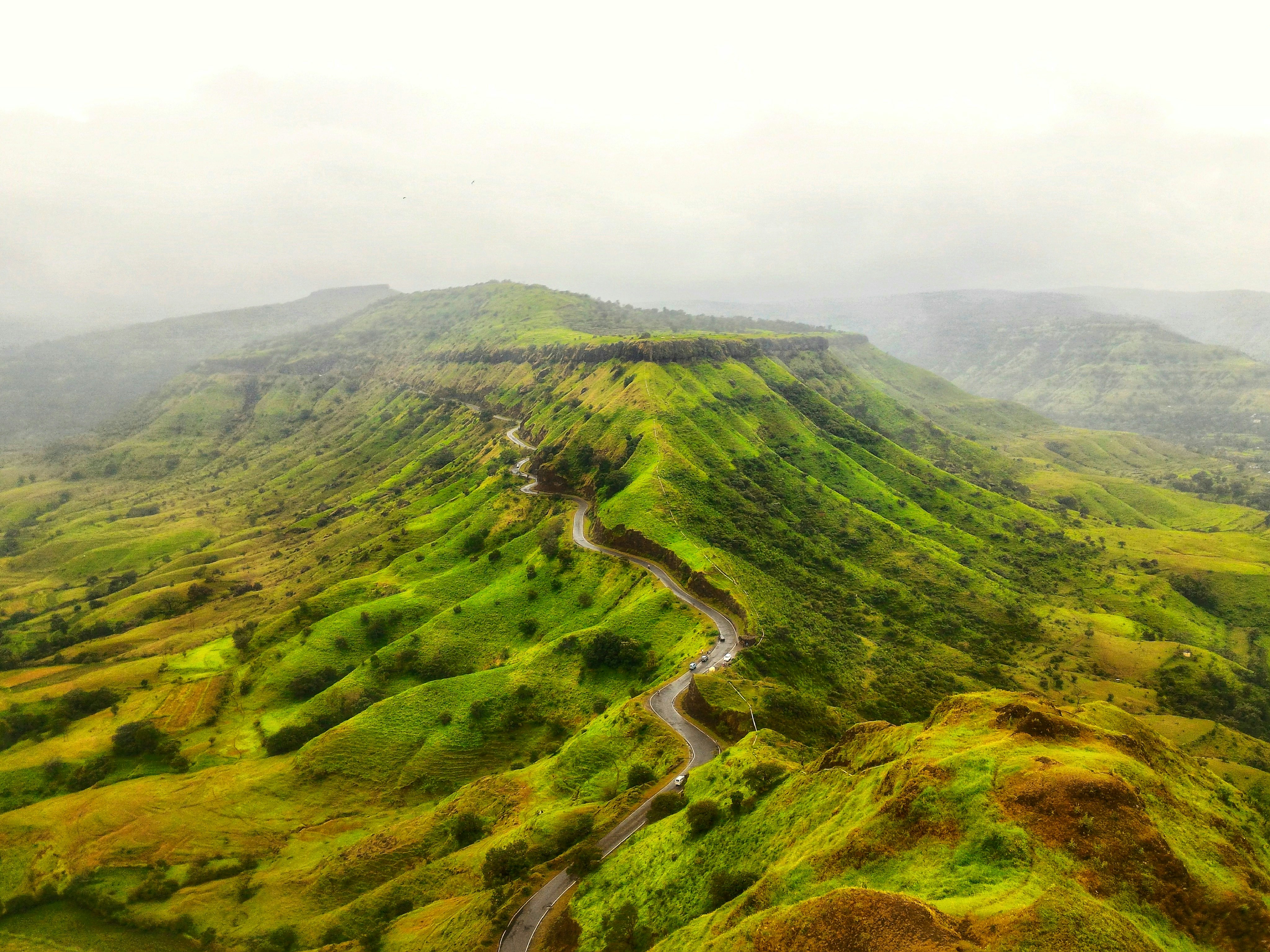 Lush green hills undulate beneath a cloudy sky, with a winding road tracing the landscape's contours.
