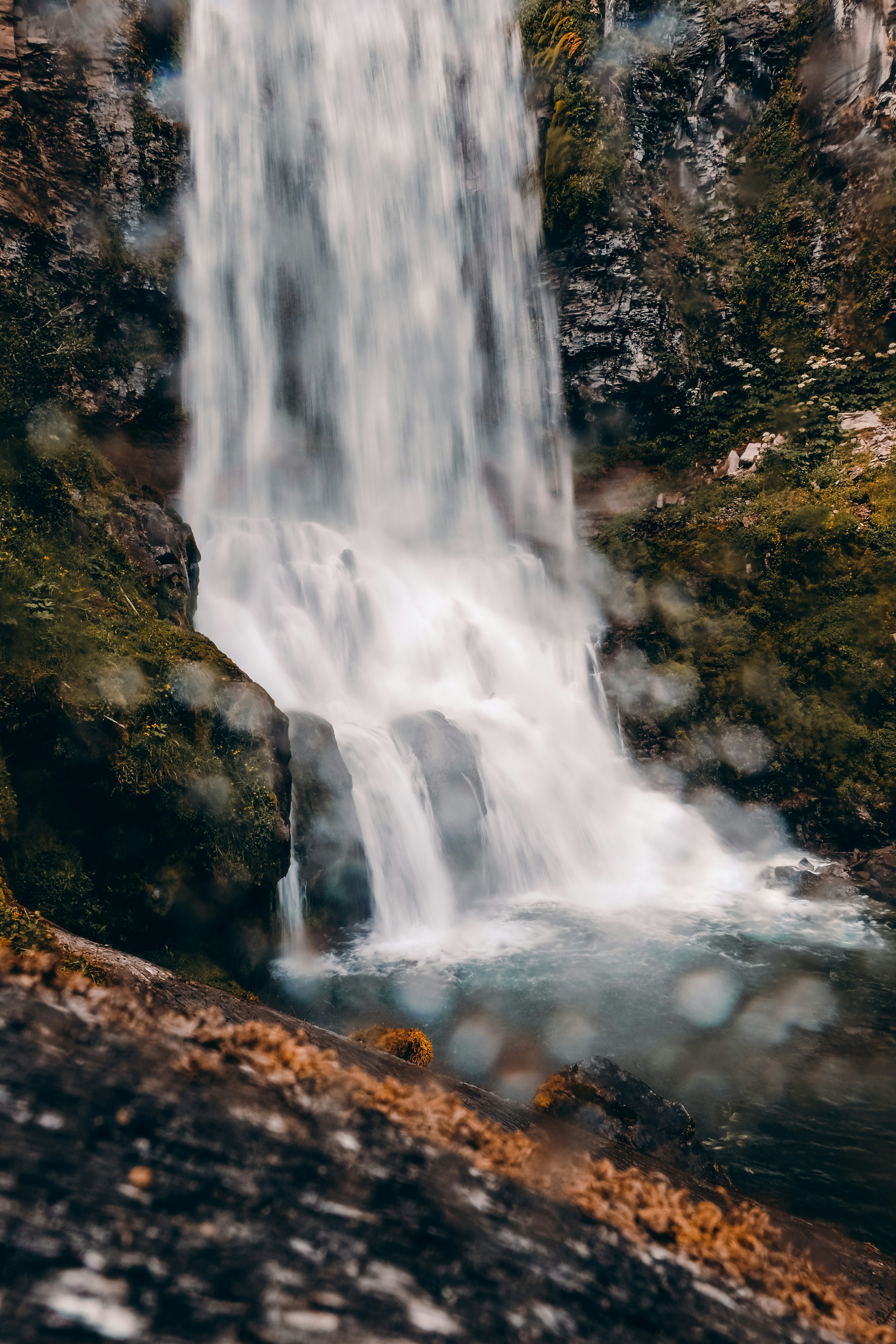 A majestic waterfall flows gracefully over rocky cliffs, surrounded by lush greenery and mist. The scene captures the serene power of nature.