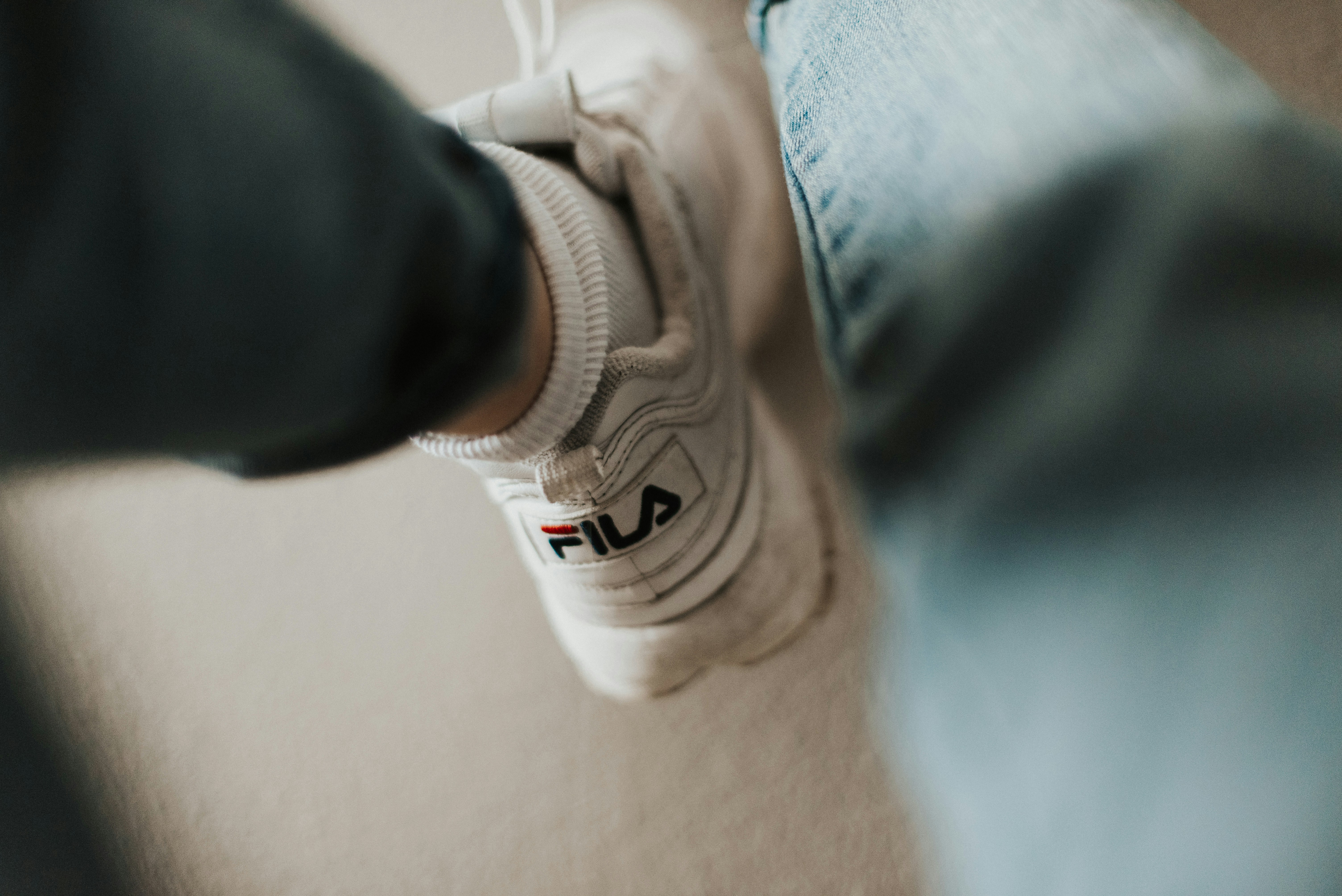 Close-up of a white sneaker resting on a surface, showcasing the brand logo and casual denim style.