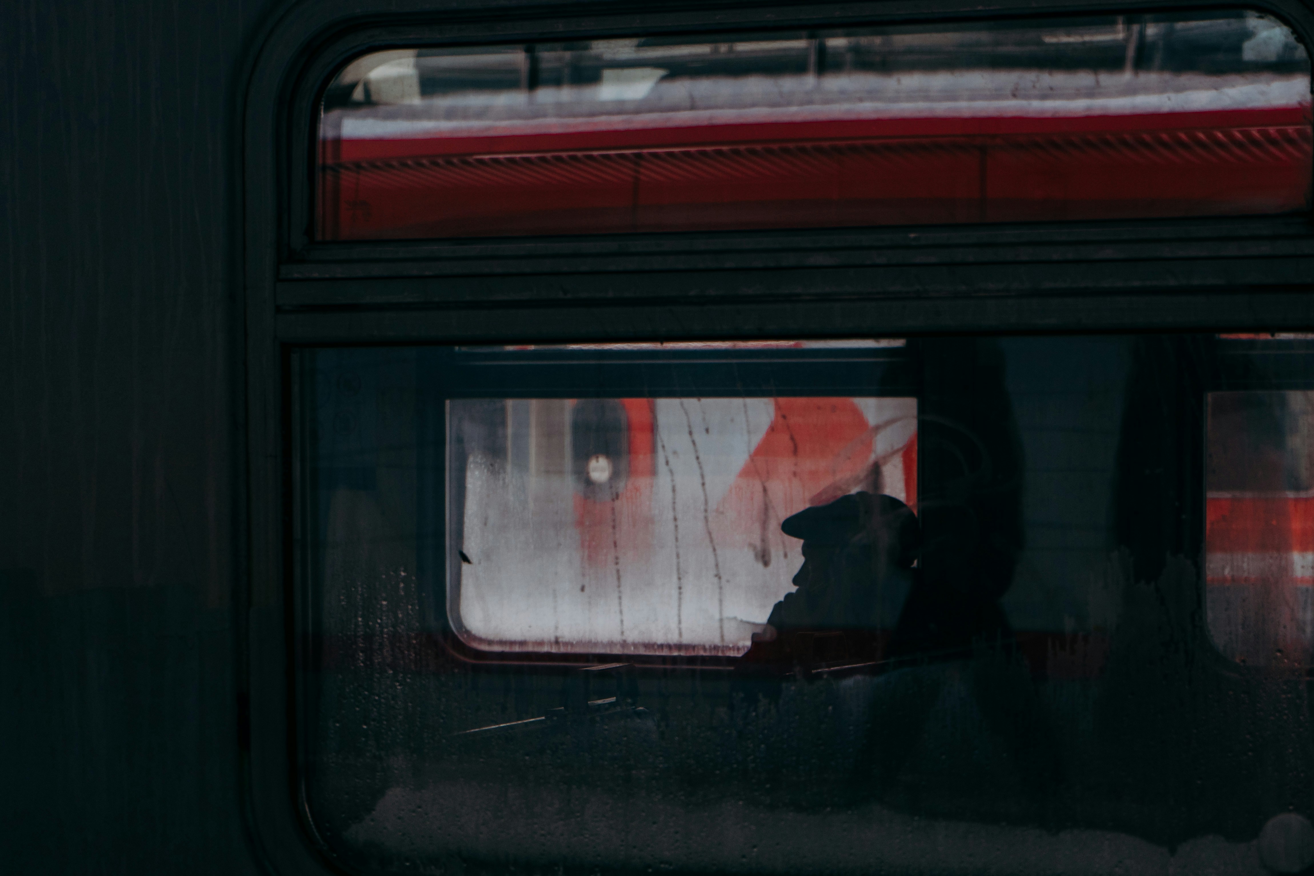 A silhouette of a person is seen through a fogged train window, with blurred red and white train elements in the background.