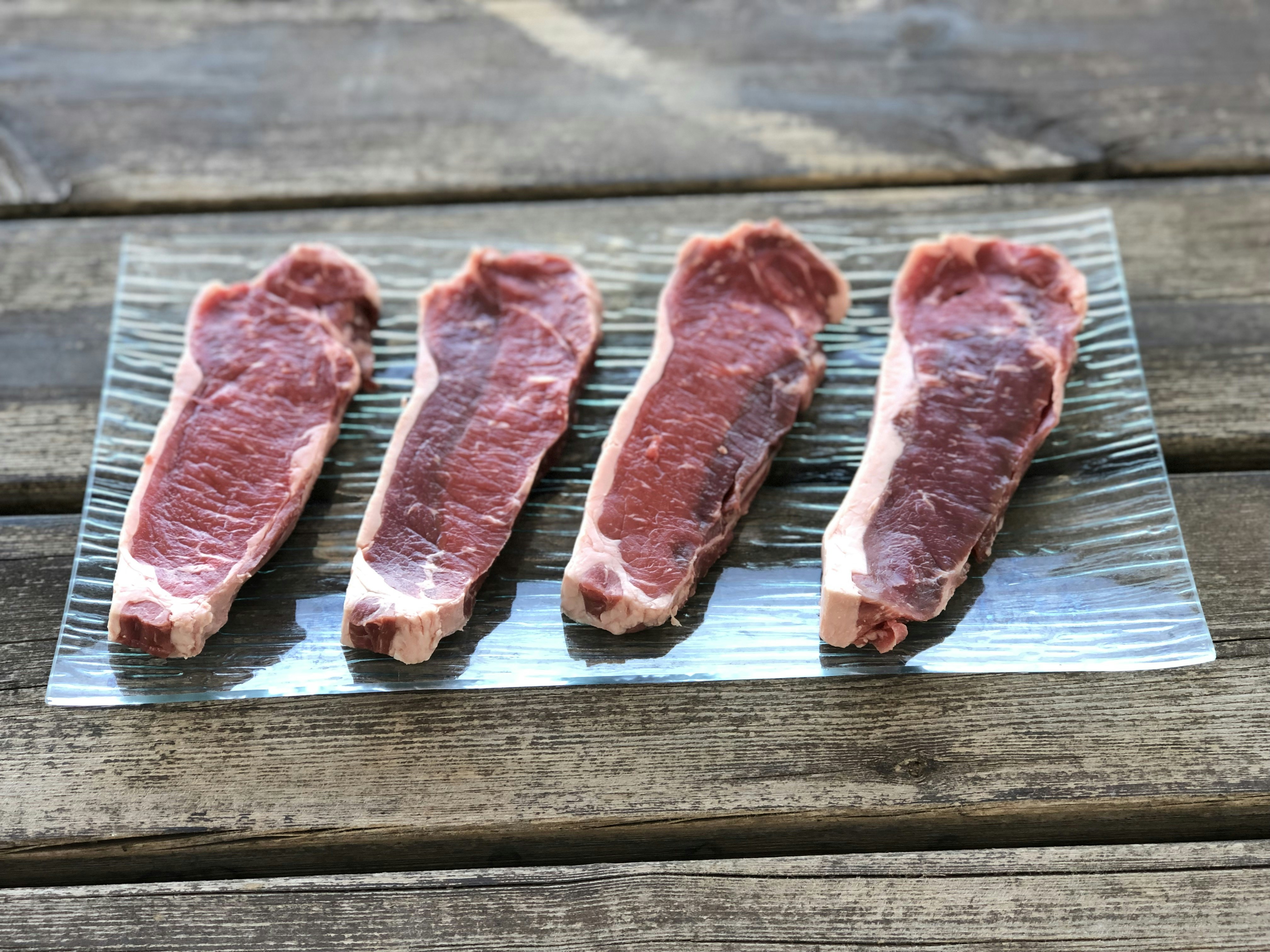 Four raw steak cuts arranged neatly on a glass platter against a rustic wooden background.