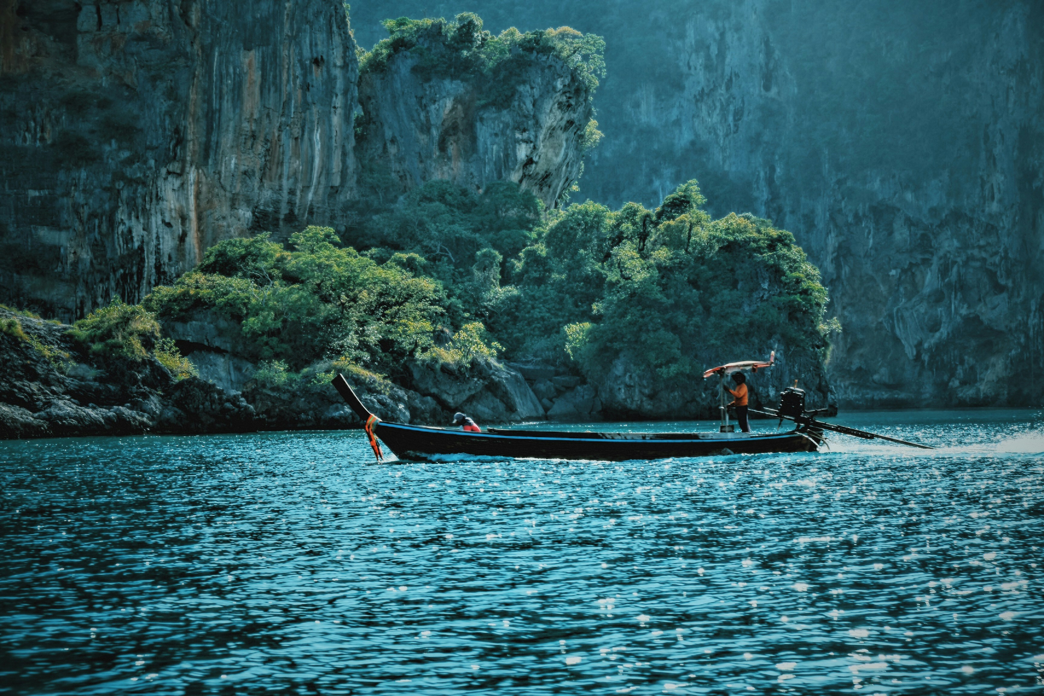 Longtail boat gliding across tranquil waters surrounded by lush cliffs and greenery.