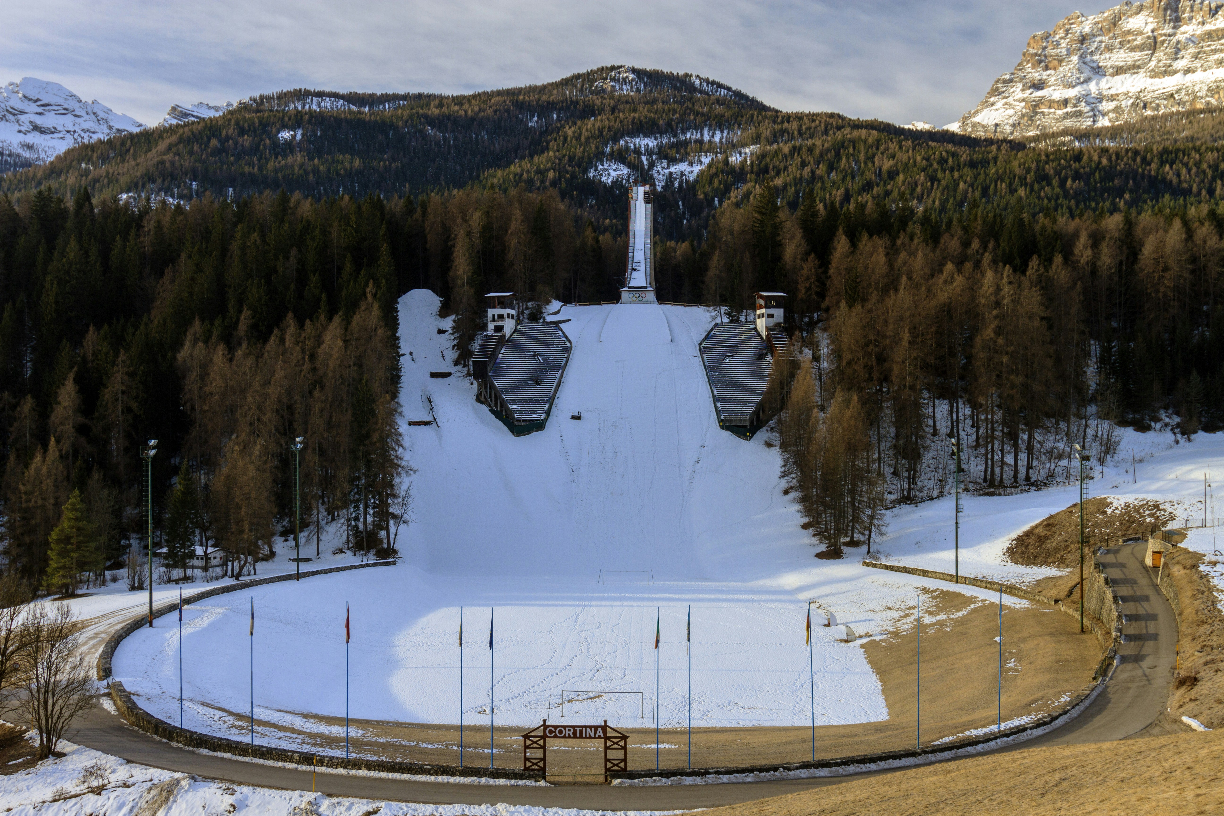 A snow-covered ski jump stands amidst a backdrop of towering mountains and dense forests, highlighting the serene beauty of winter sports venues.
