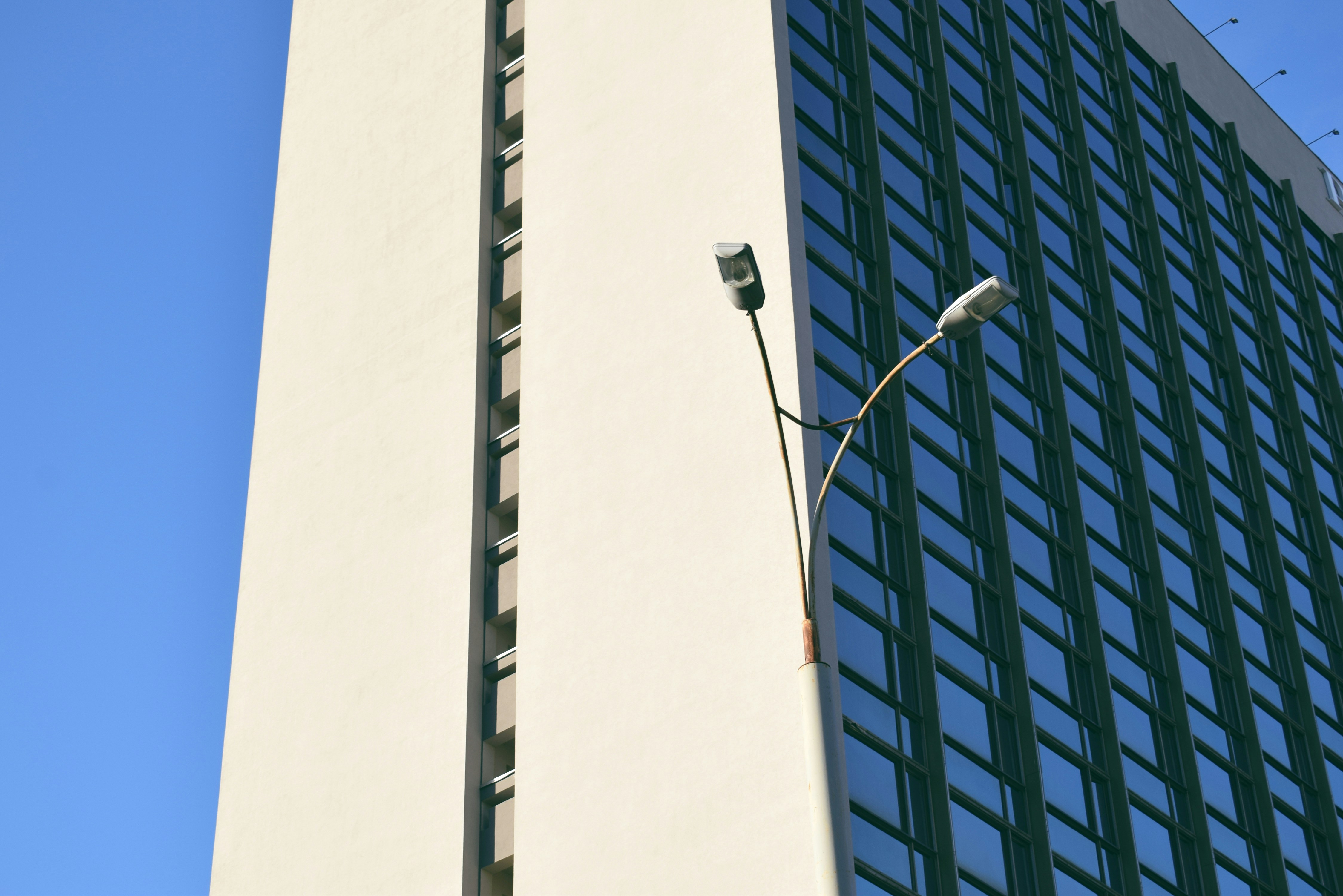 Tall modern building with reflective glass windows and a street lamp in the foreground against a clear blue sky.