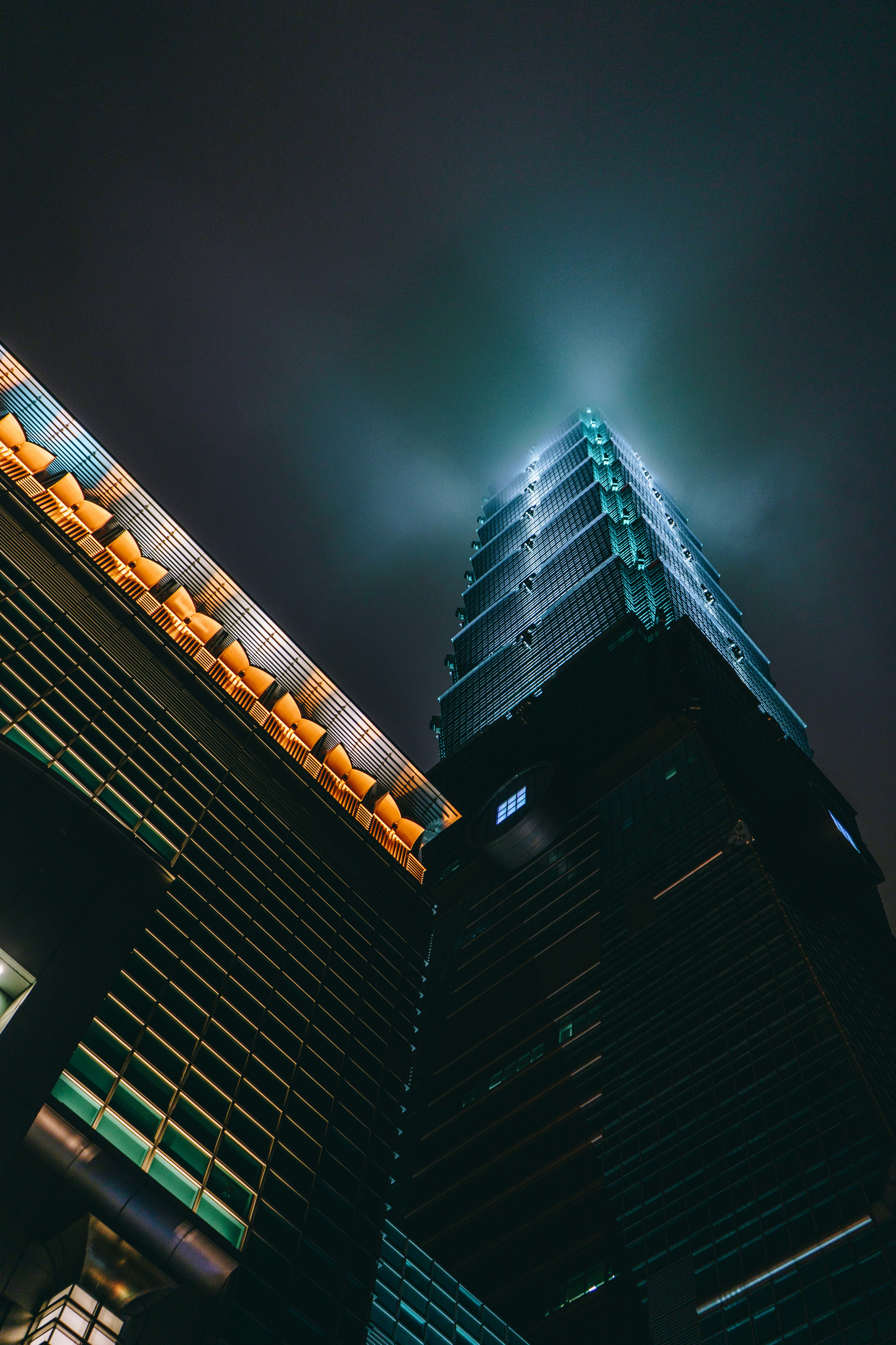 Illuminated skyscraper piercing through a cloudy night sky, showcasing modern architectural design and vibrant lighting.