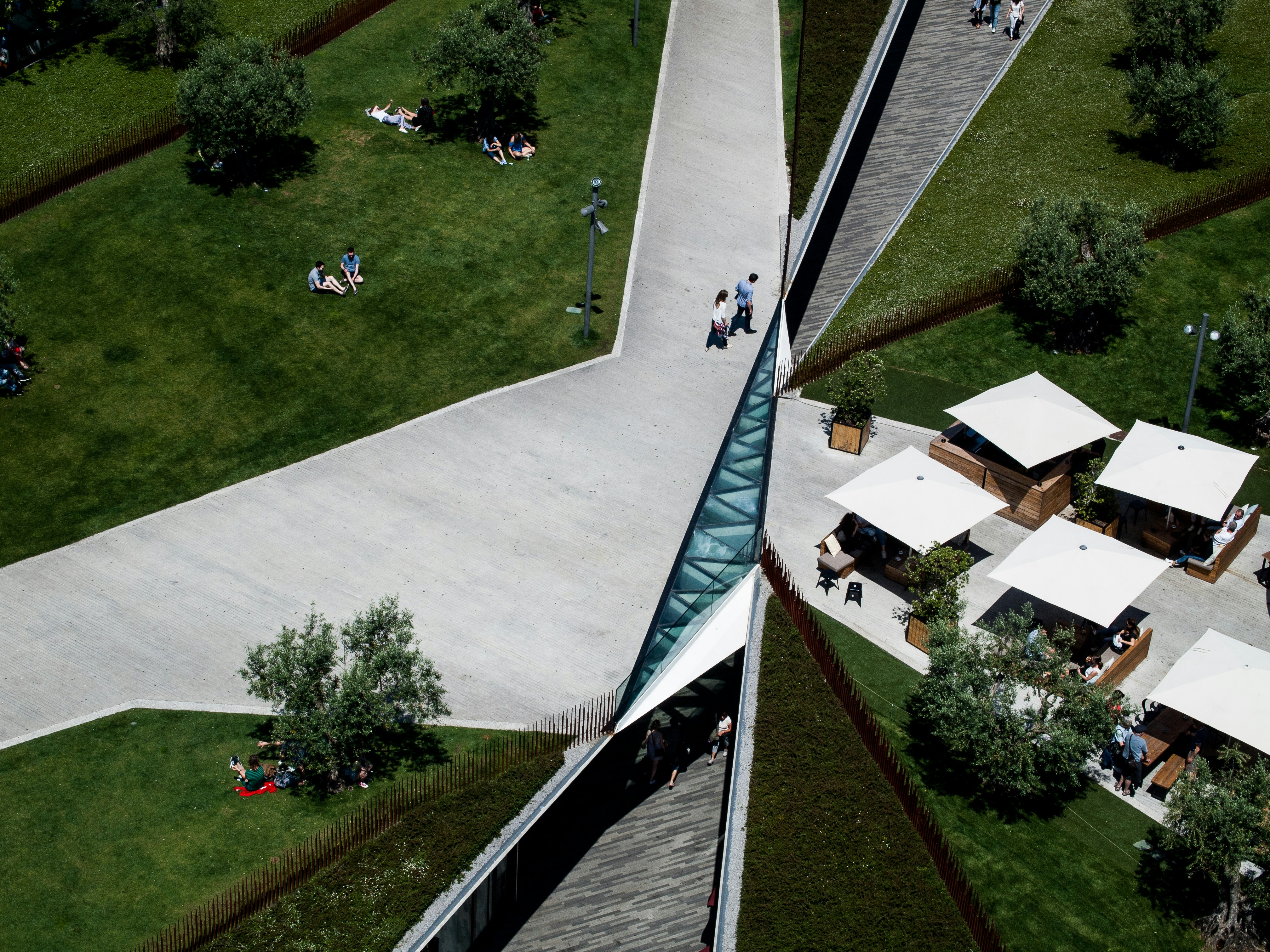 Aerial view of an urban park featuring intersecting pathways, people enjoying the space, and stylish outdoor seating areas under white canopies.