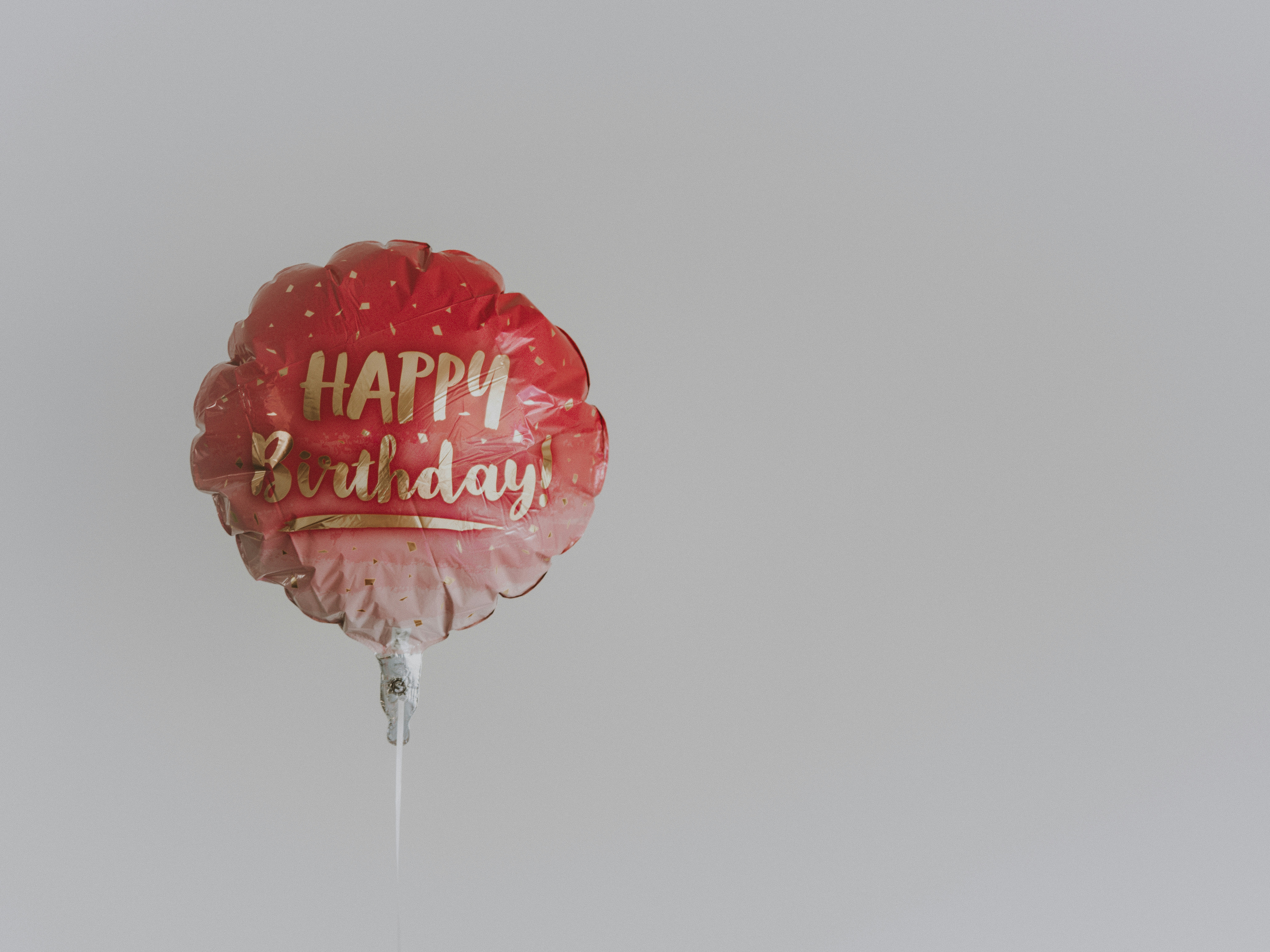 A vibrant red balloon with 'HAPPY Birthday!' printed in gold, floating against a neutral background.