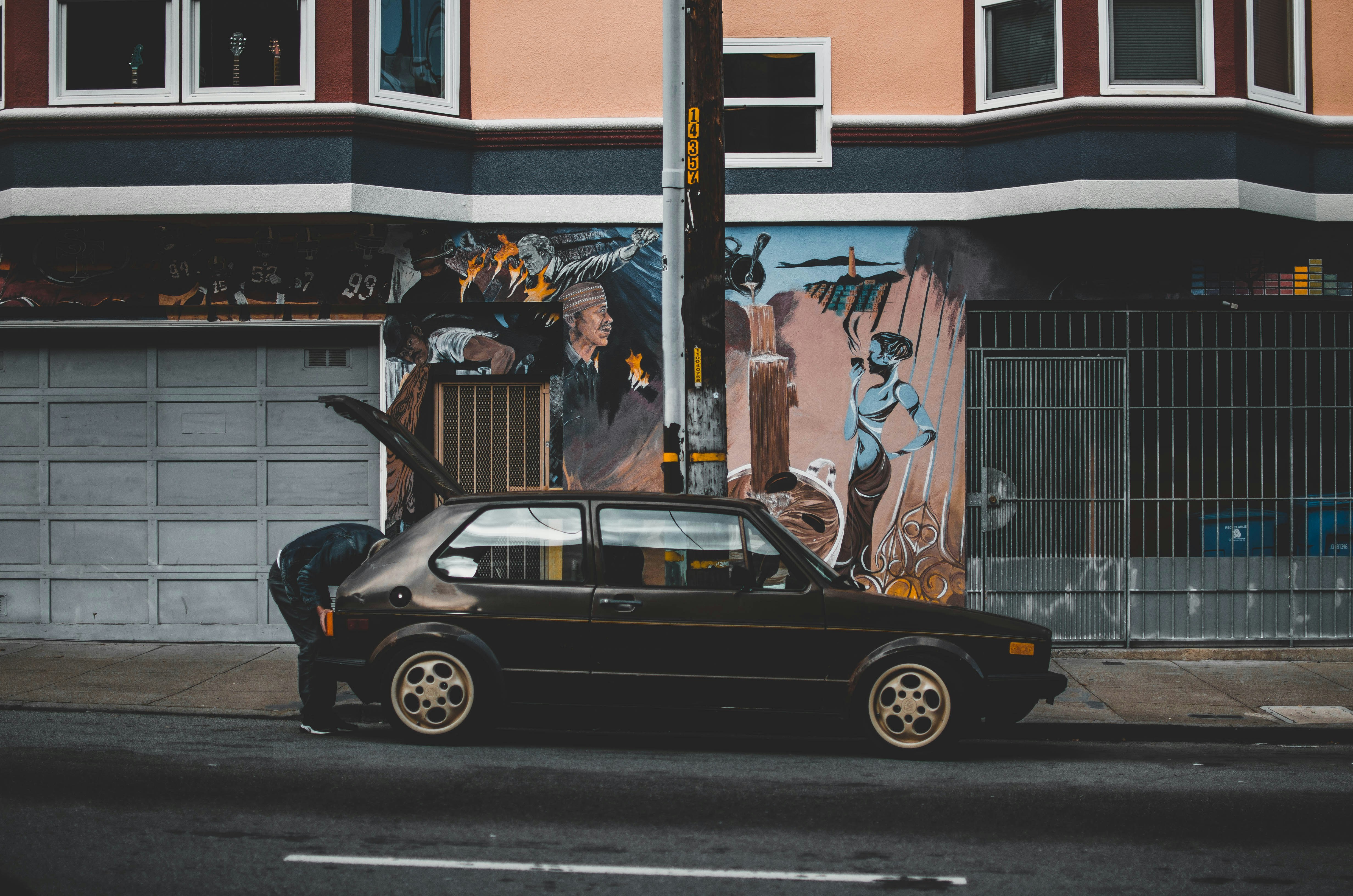 Classic black hatchback parked beside a colorful mural showcasing urban art and culture.
